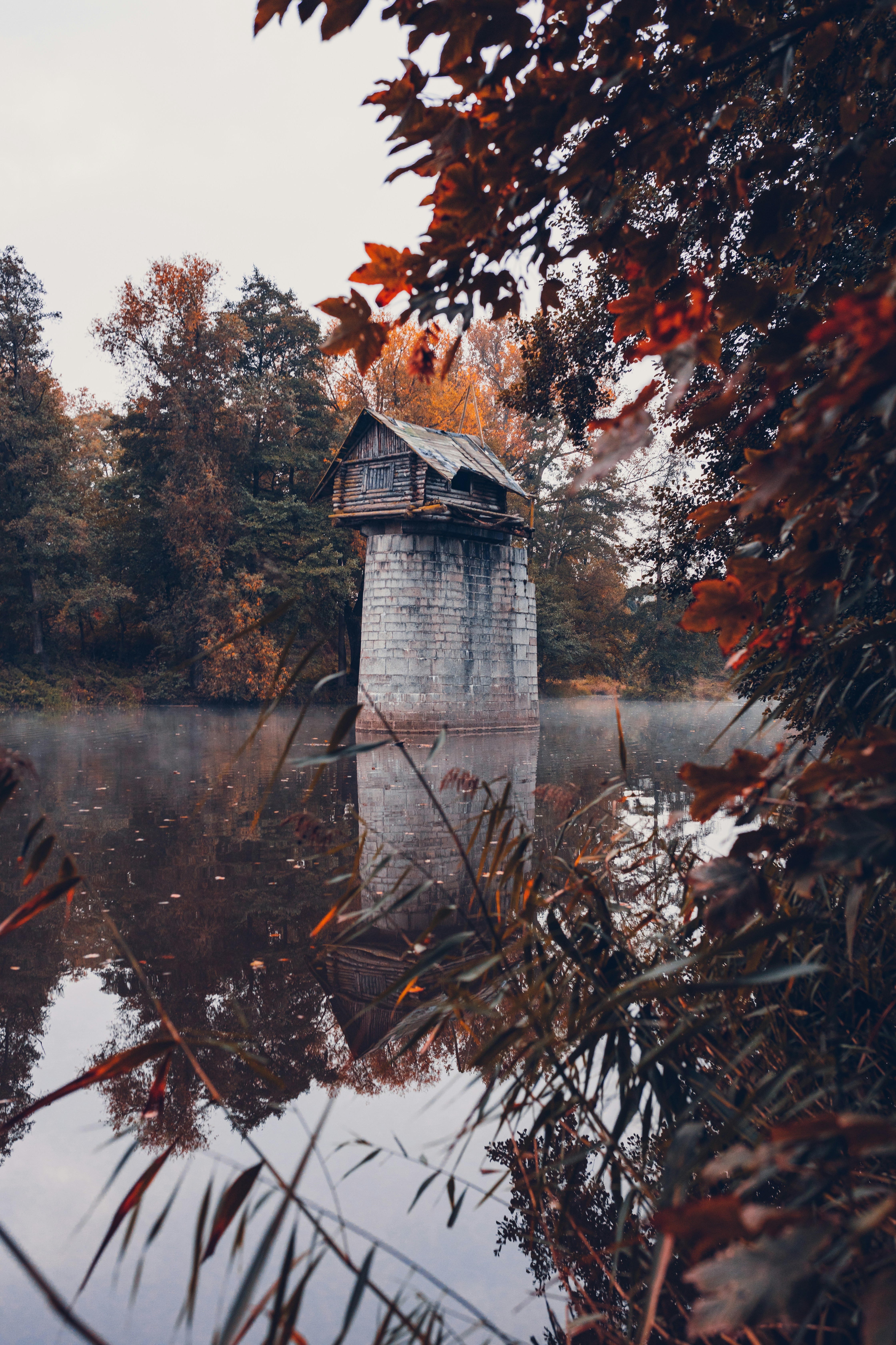 Autumn's Sentinel: A Weathered House on a Concrete Pillar in a Quiet Lake