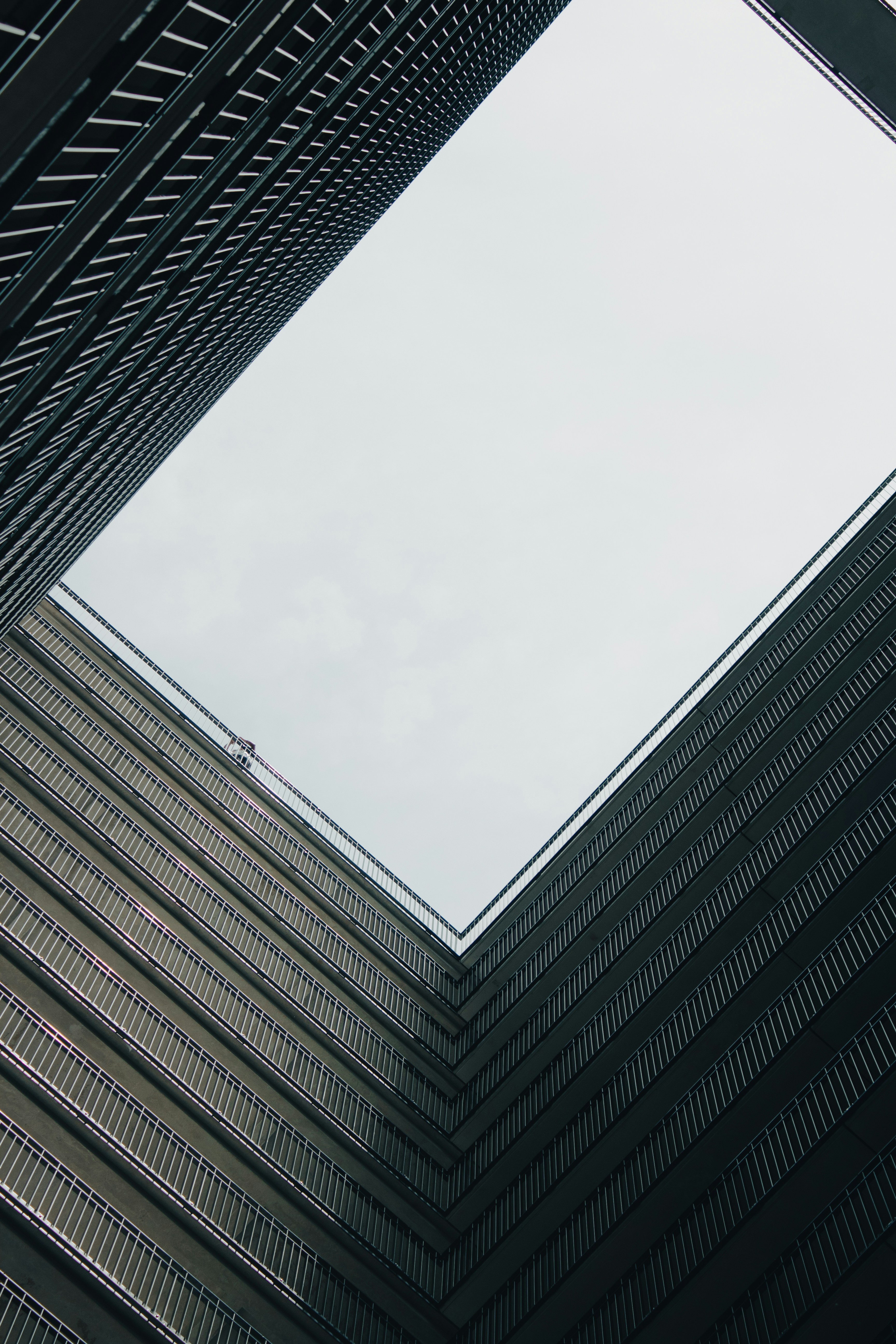View from the ground looking up at a modern building's open atrium, framed by stark lines and a cloudy sky above.