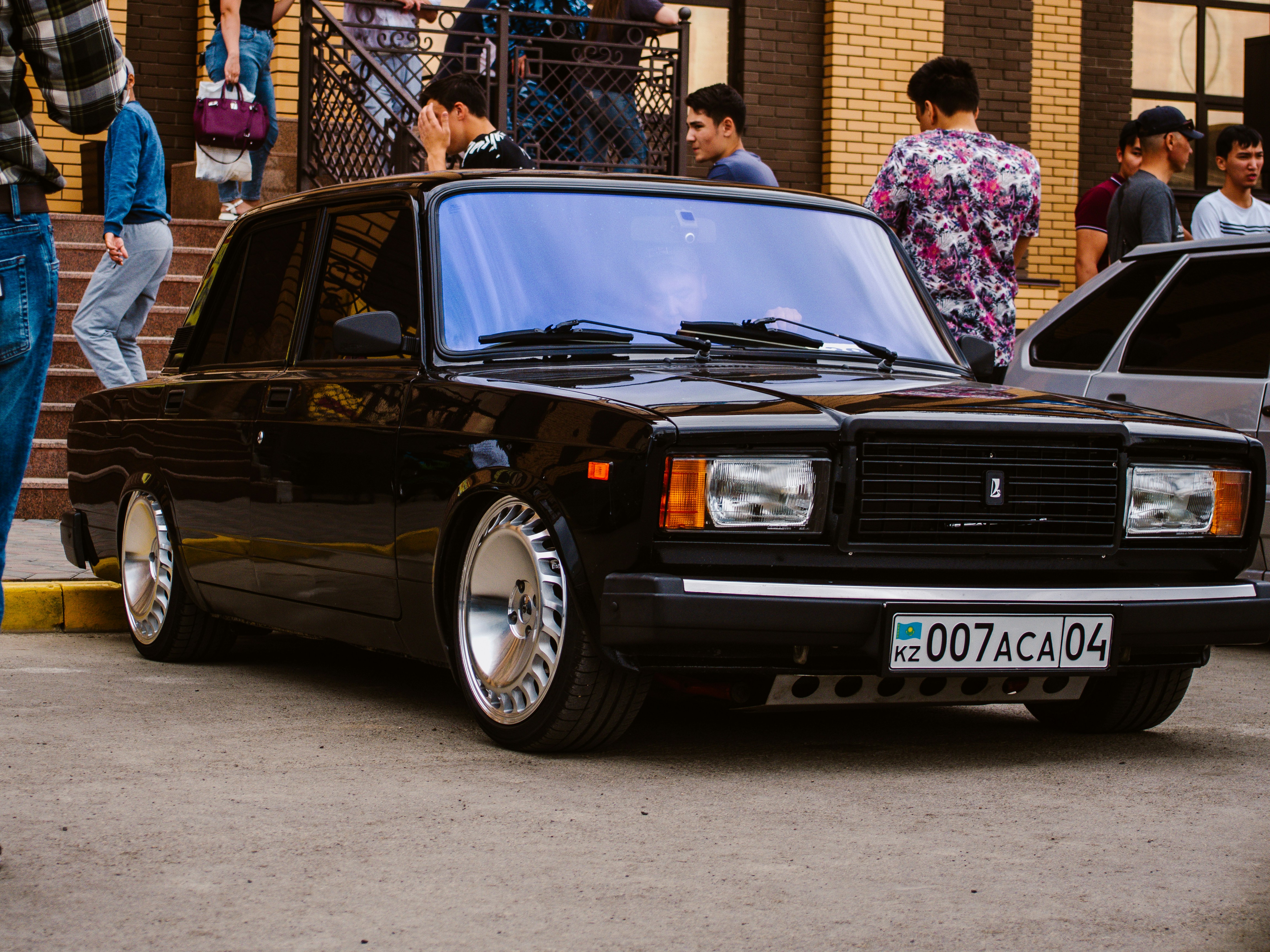 Sleek black vintage car parked on a city street with people in the background.