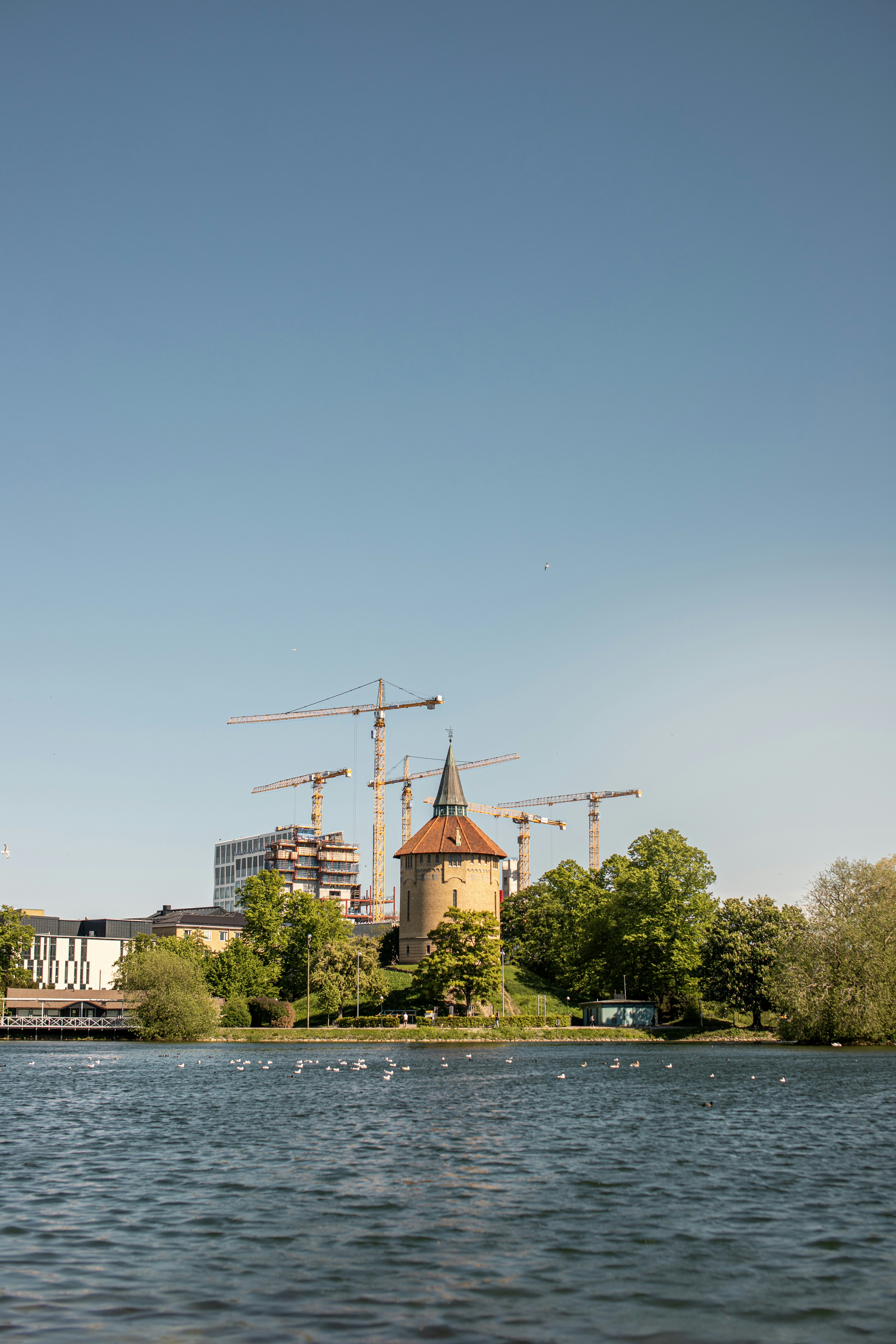 Red-Topped Turret and Rising Cranes Over a Tranquil Lakeside