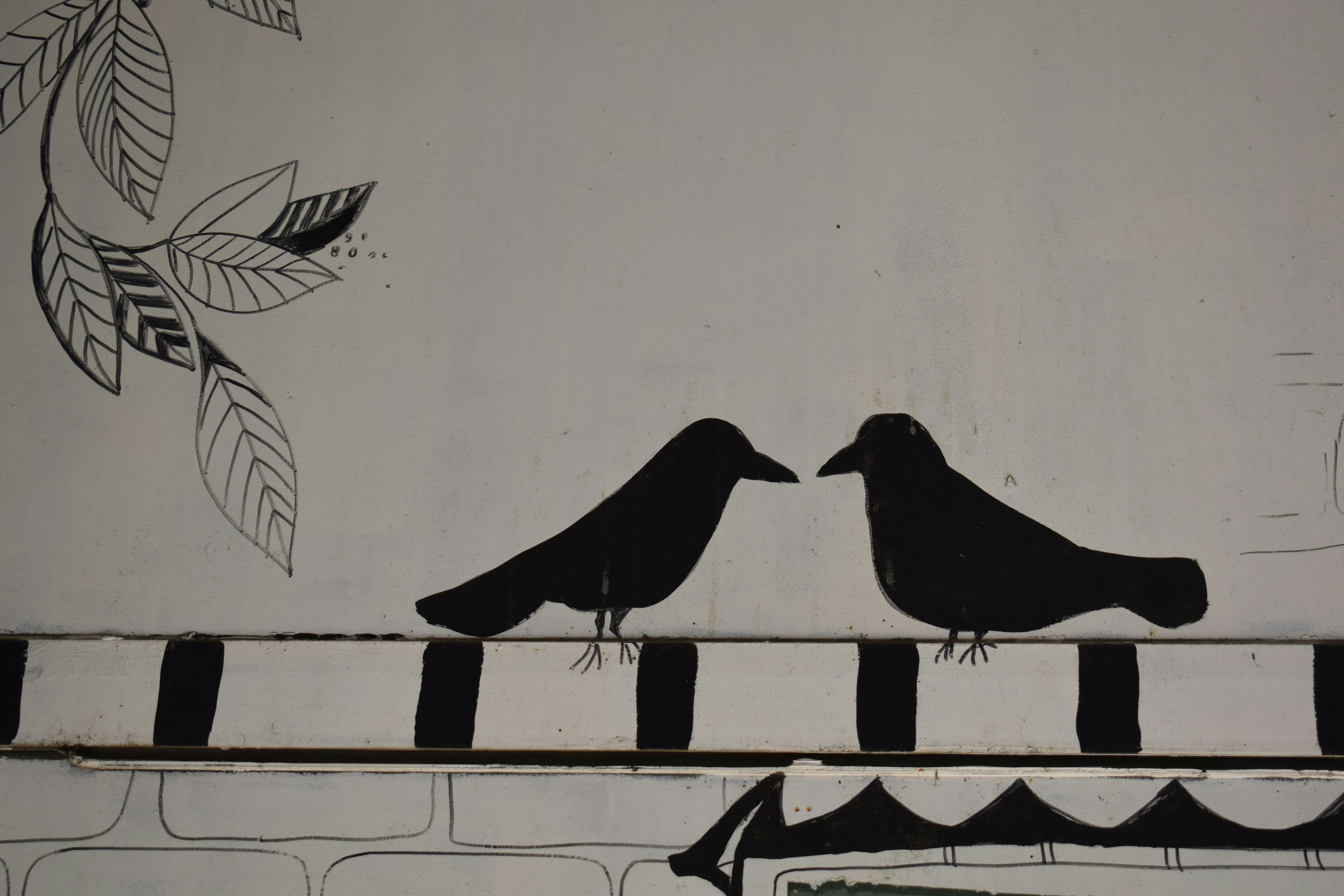 Two black silhouette birds perched on a ledge, surrounded by minimalistic leaf designs on a white wall.