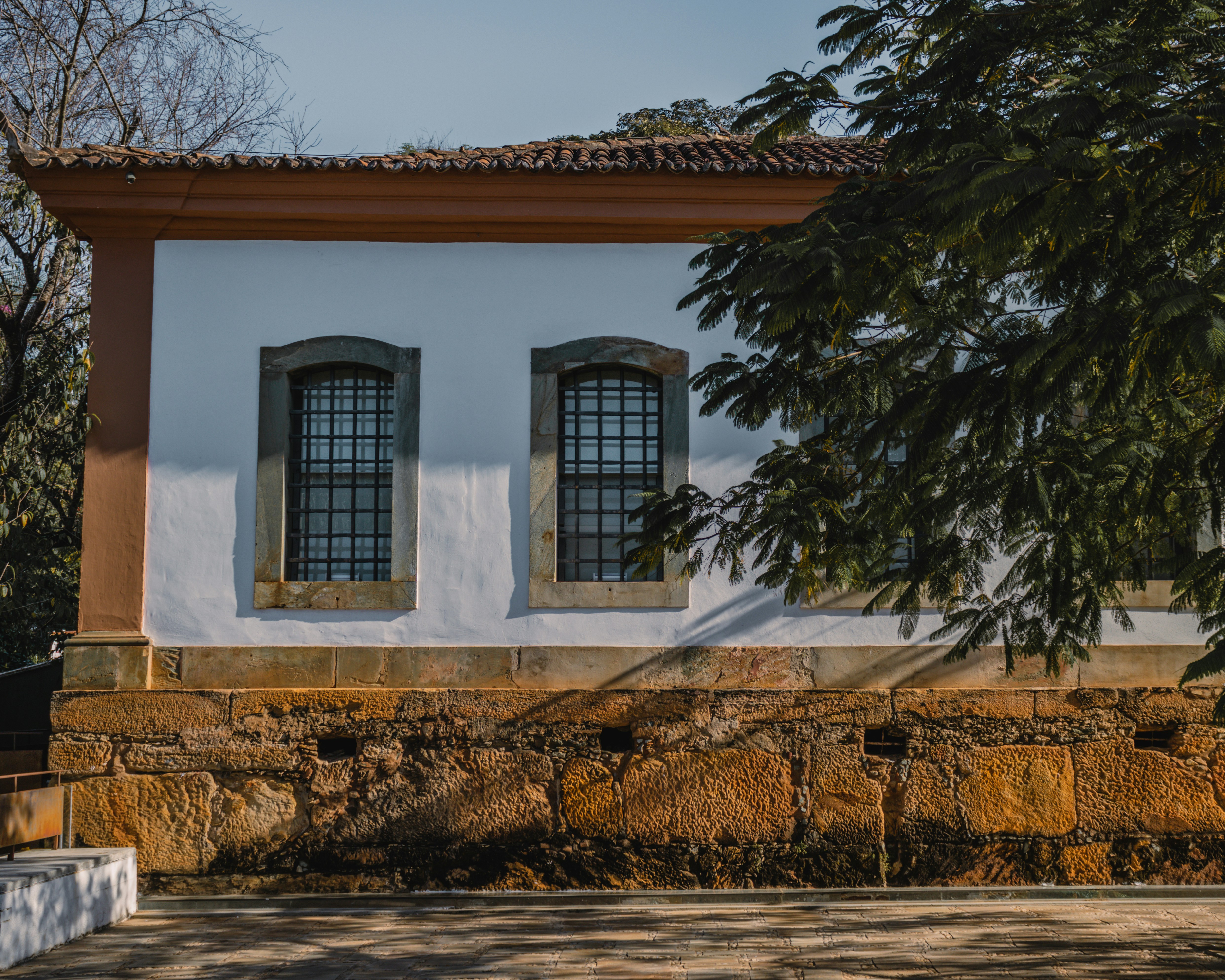 Historic building showcasing a blend of stone and whitewashed walls, framed by lush foliage and intricate window designs.