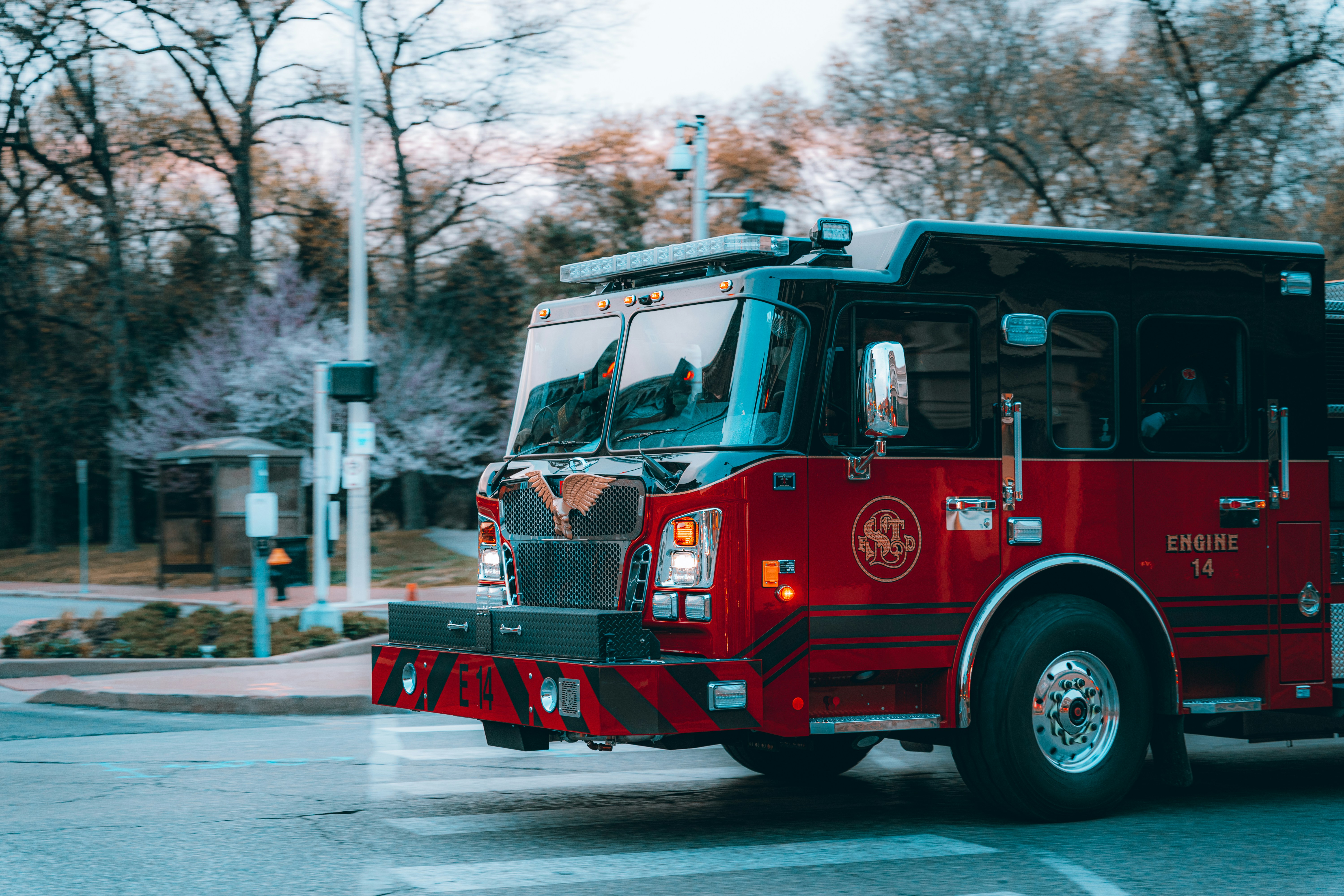 Fire engine navigating through an urban intersection, showcasing emergency readiness. The vehicle is prominently displayed against a backdrop of springtime trees.