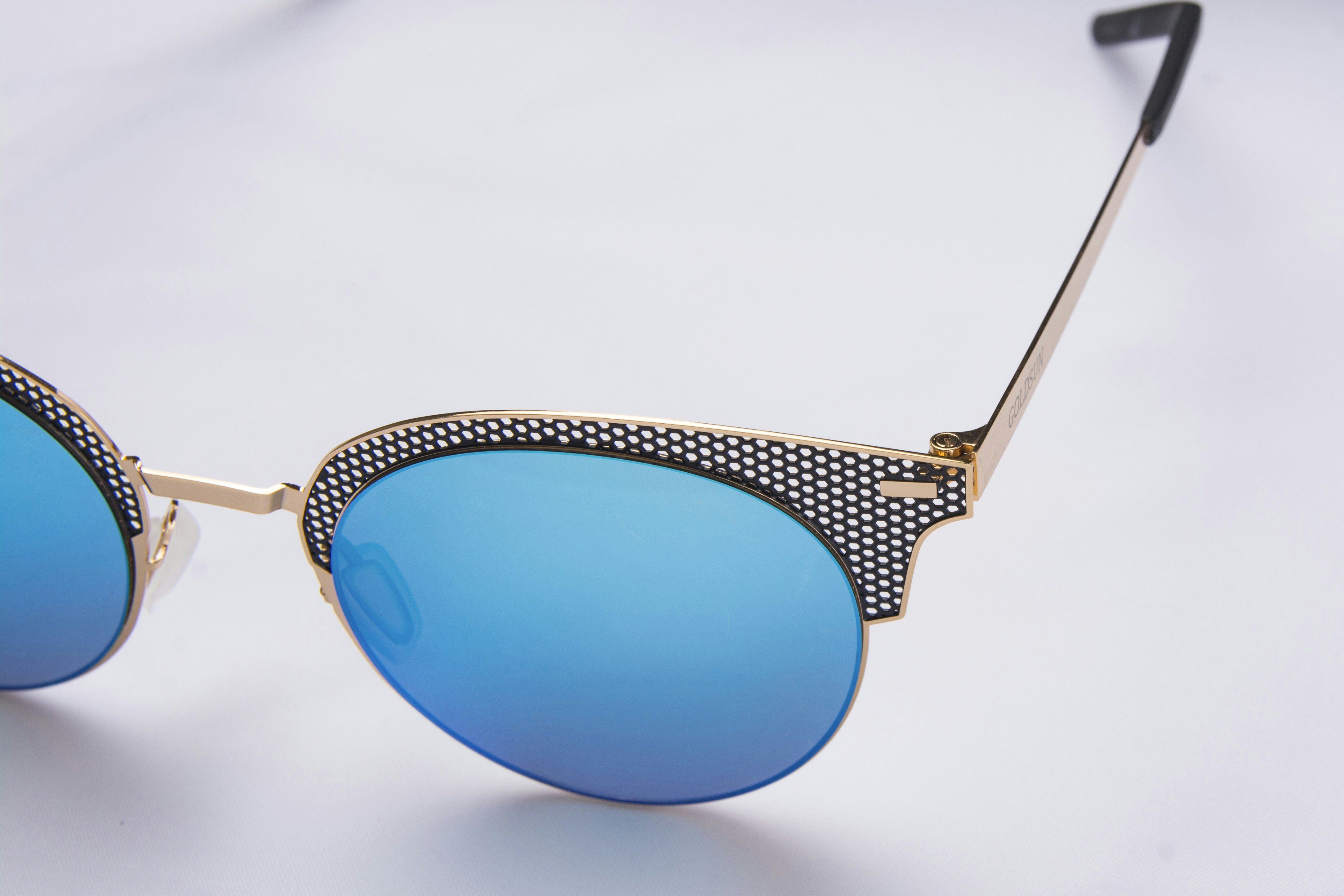 Blue Mirage: Close-Up of Perforated Gold Sunglasses on White Studio Surface