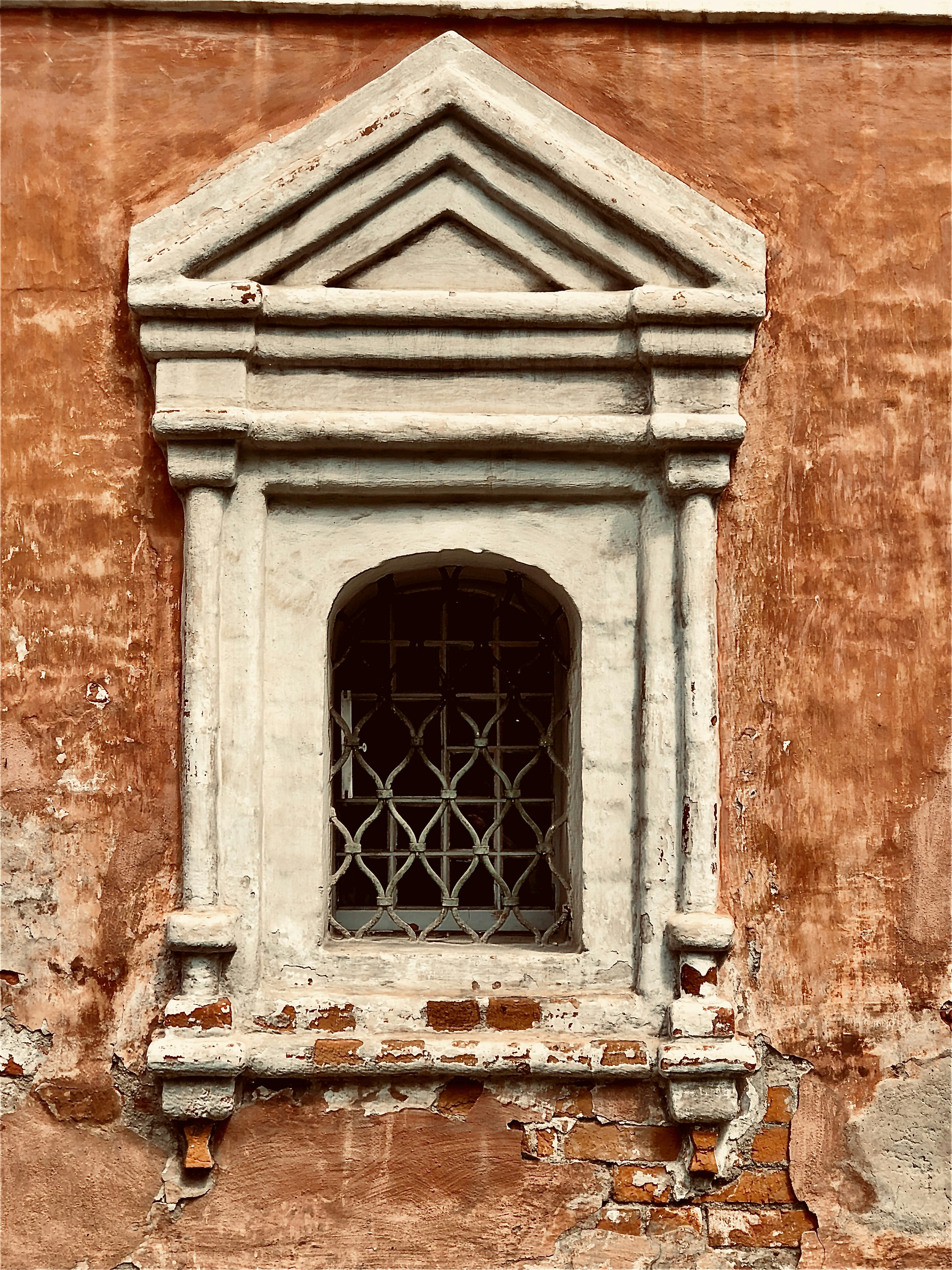 Architectural detail of a weathered window frame with intricate designs set against a textured, orange wall.