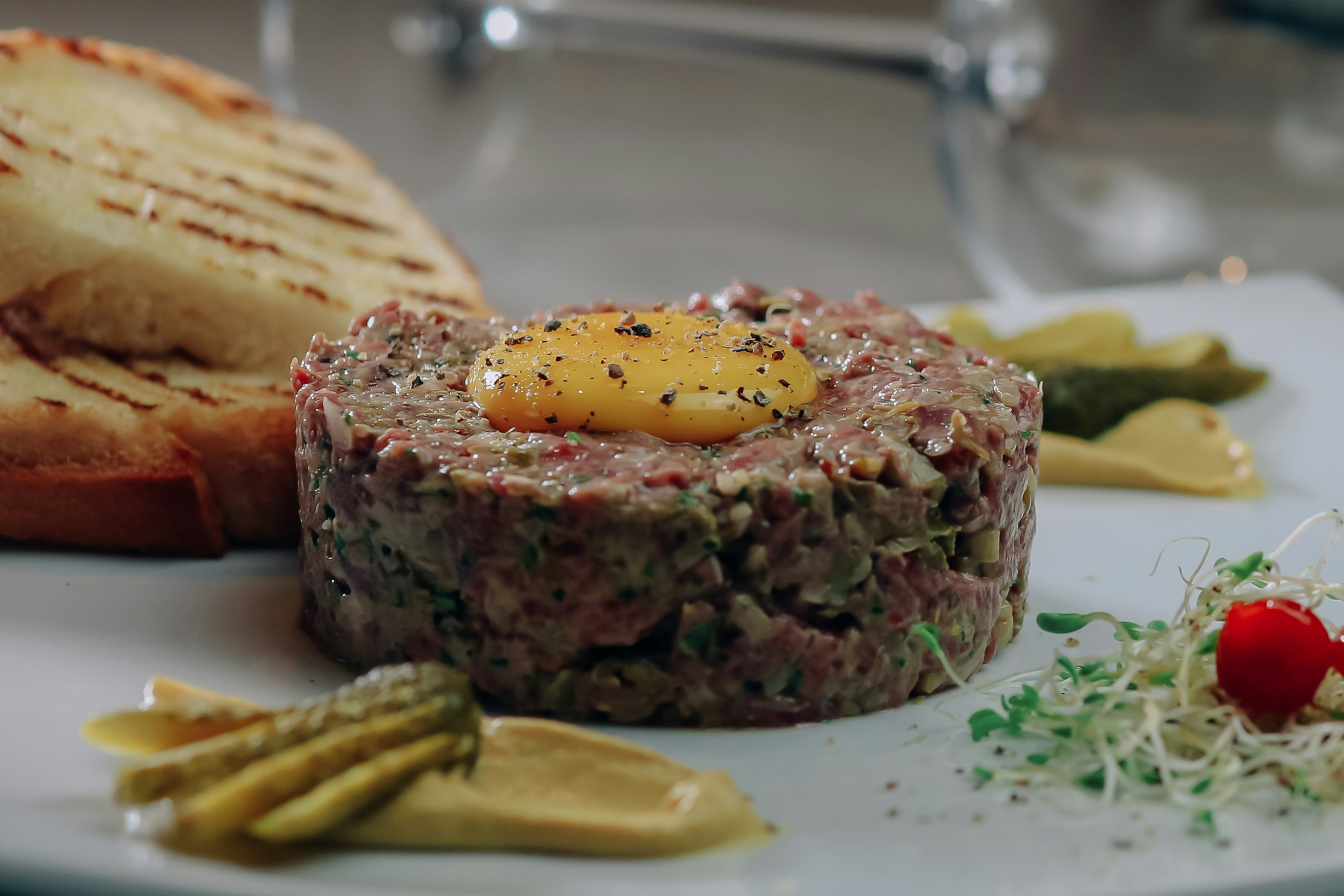 Gourmet beef tartare garnished with a quail egg yolk, accompanied by pickles and toasted bread. A feast for the senses.