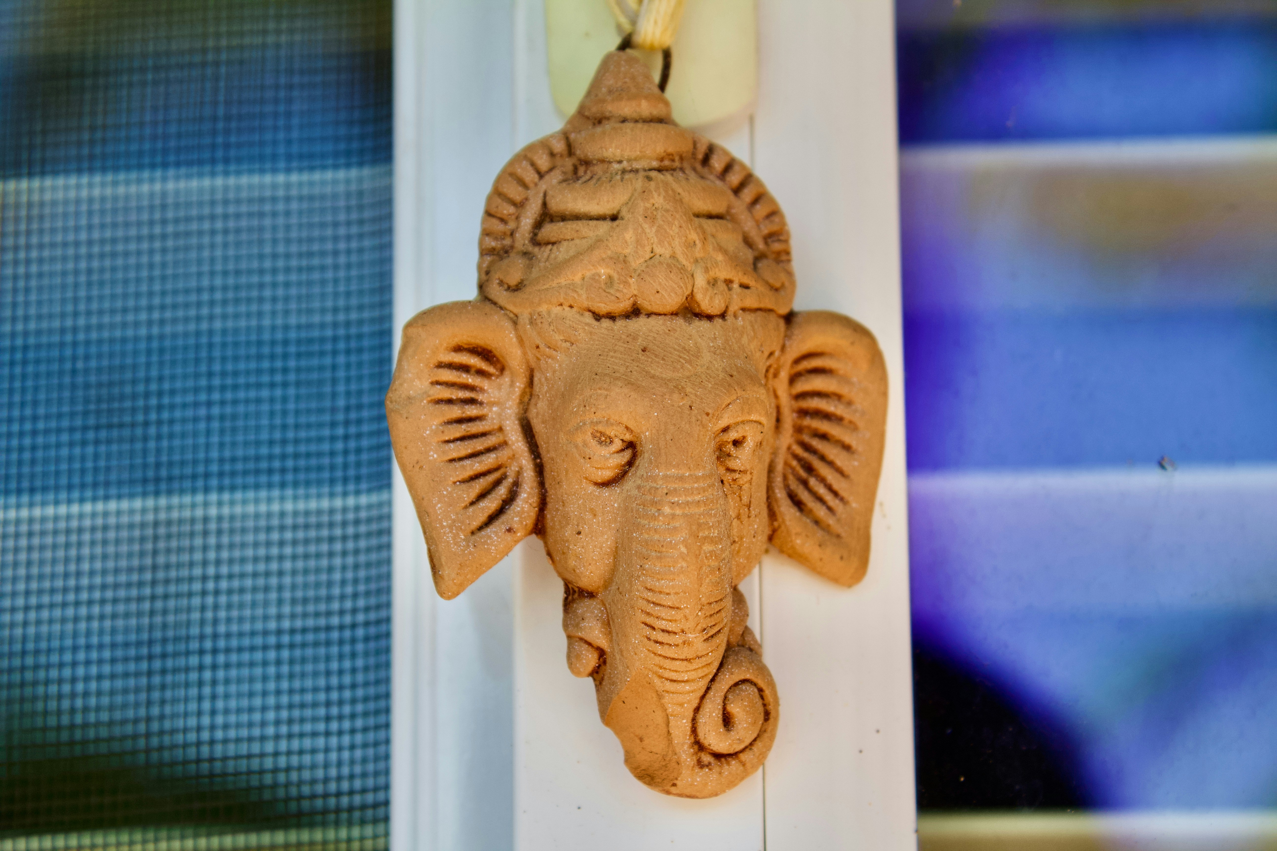 Intricately crafted clay Ganesha head hanging against a textured background, showcasing traditional artistry. 