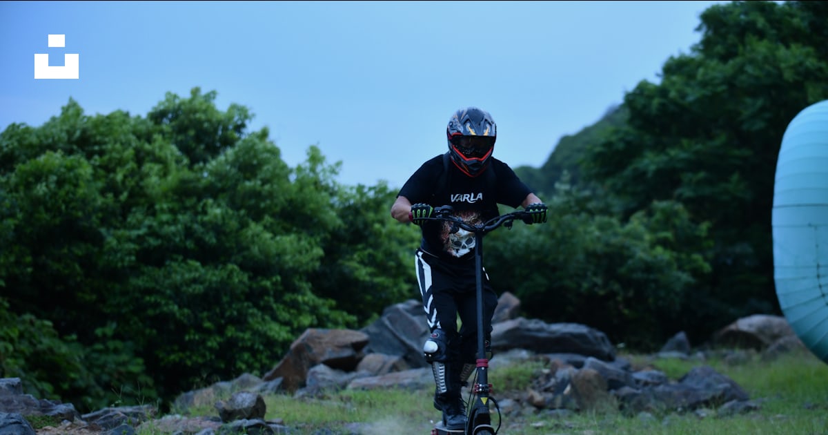 昼間、緑の芝生の野原で自転車に乗る黒いヘルメットをかぶった男の写真 Unsplashのオフロード用スクーターの無料画像
