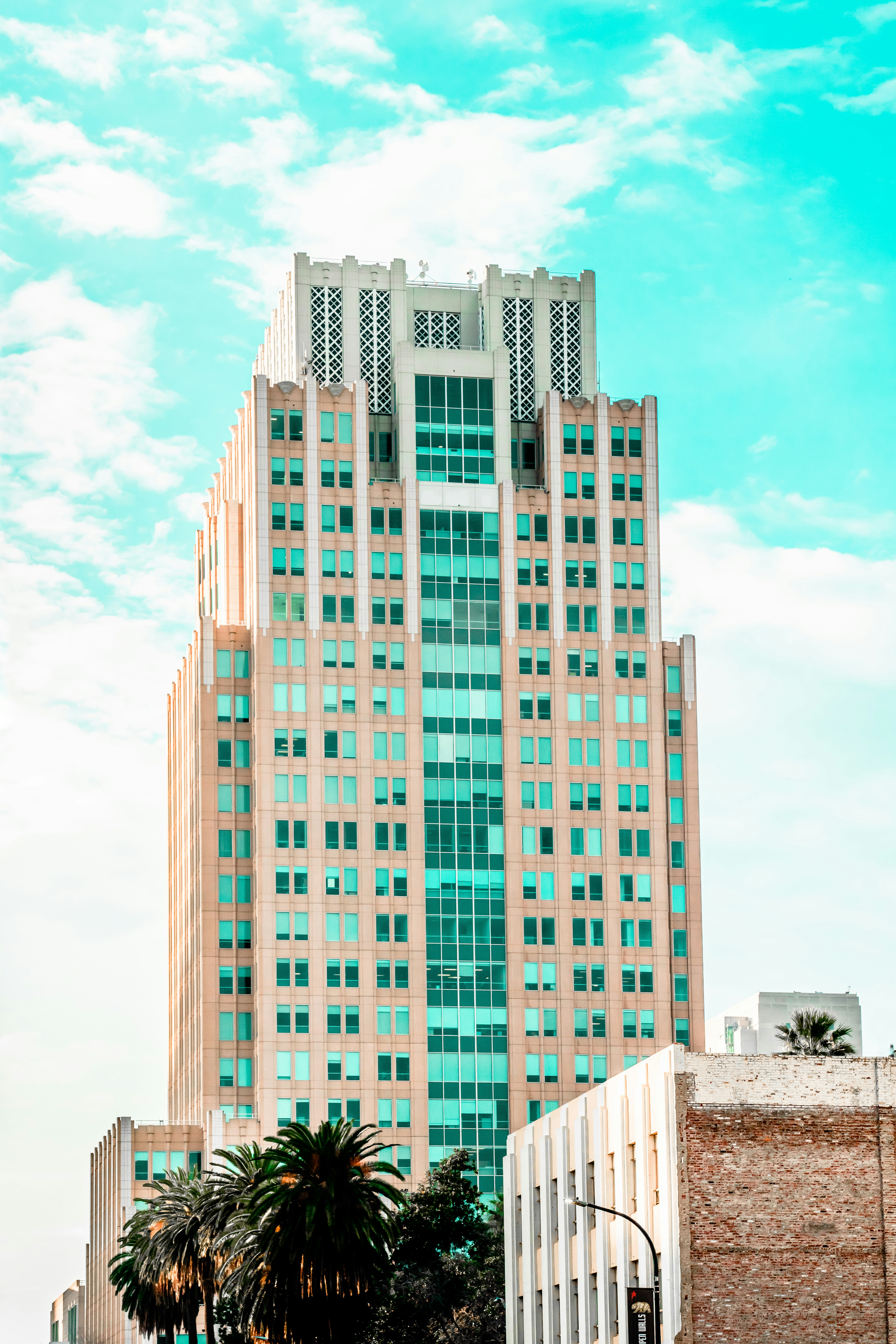 A striking skyscraper with a blend of glass and art deco elements, surrounded by palm trees against a bright blue sky.