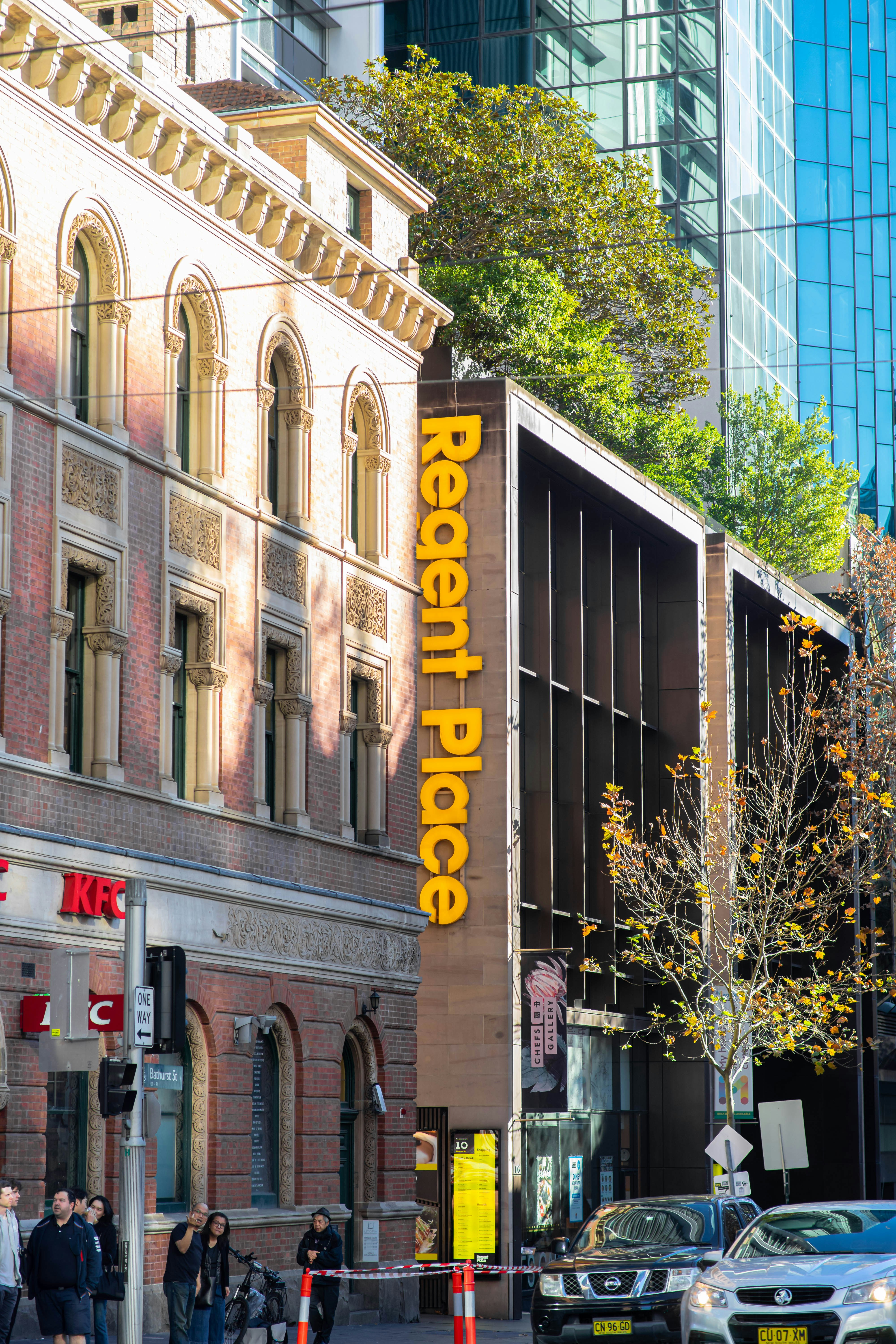 Historic building juxtaposed with contemporary architecture, showcasing the 'Regent Place' sign amid urban life.