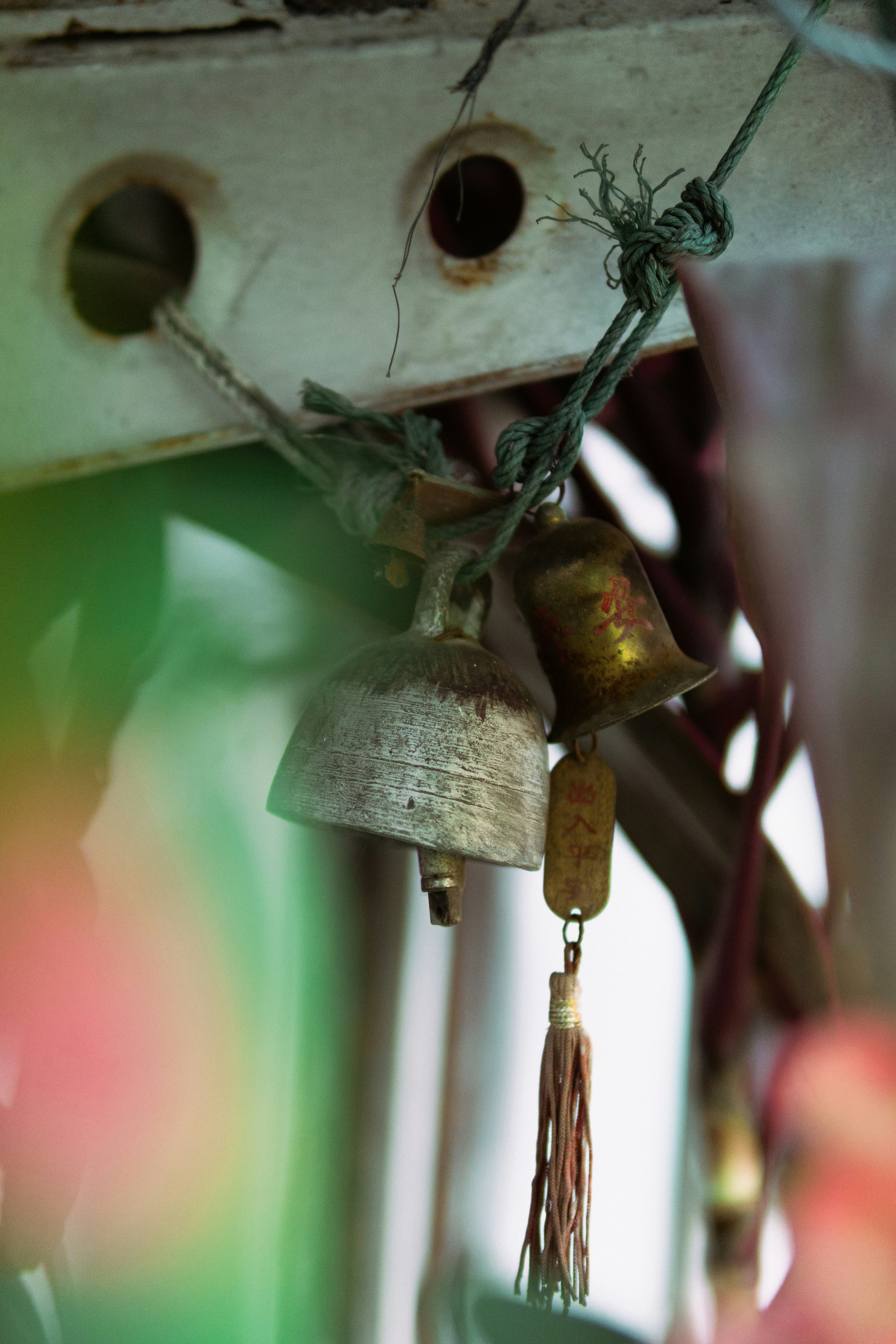 Intricately designed bells hang from a rustic wooden structure, surrounded by soft greenery and hints of color, evoking a sense of nostalgia.