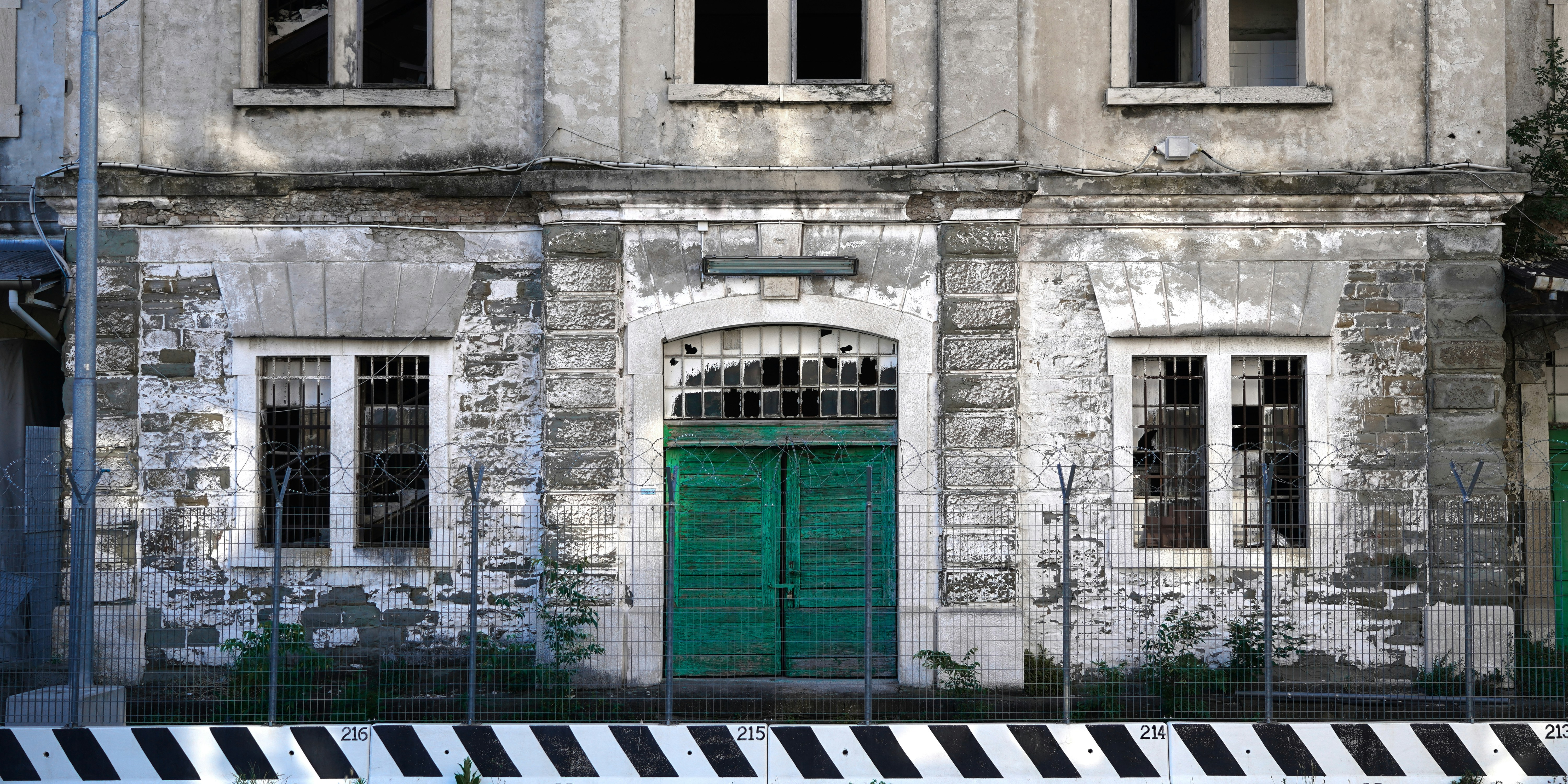 A weathered concrete building with a vibrant green wooden door and barred windows.
