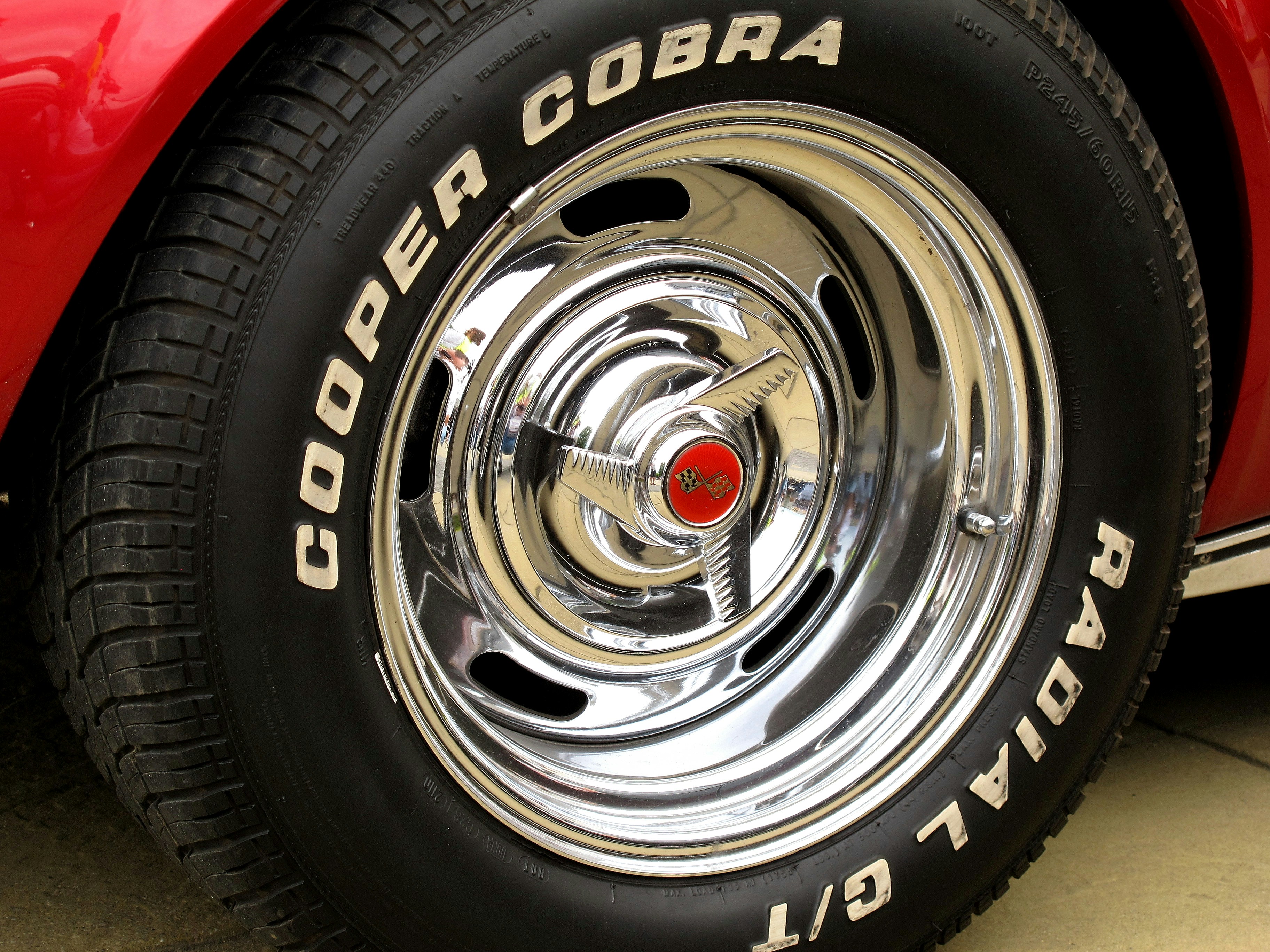 Close-up of a polished chrome wheel on a red Chevrolet Corvette C3, featuring Cooper Cobra radial tires.