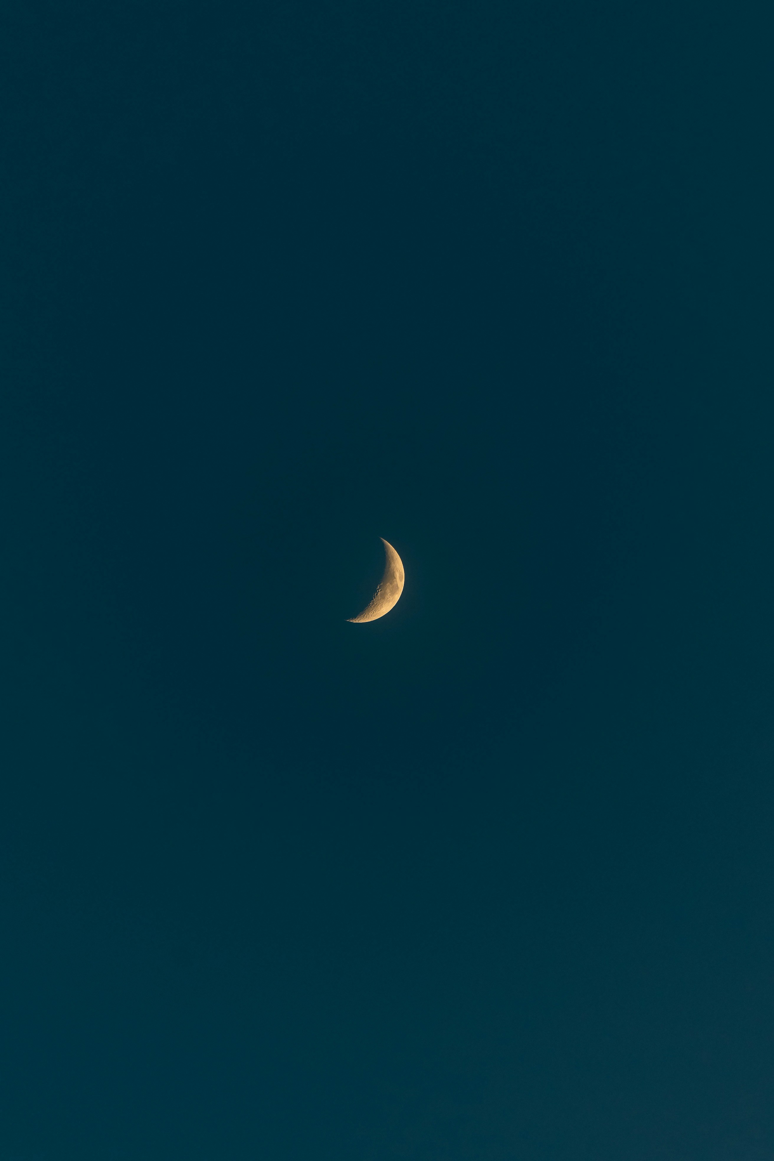 Crescent moon softly illuminated against a deep blue sky, evoking a serene nighttime atmosphere.