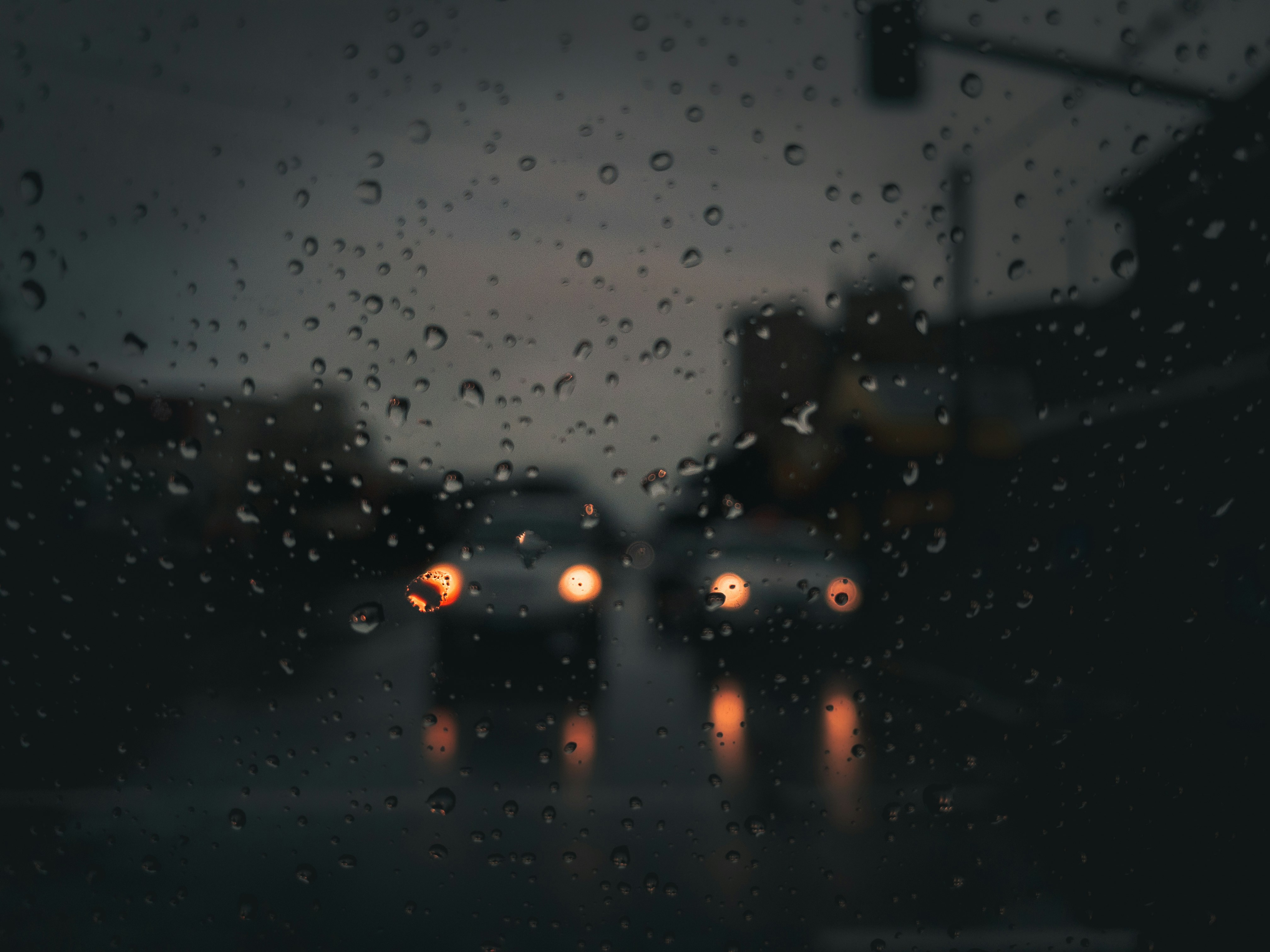 Two cars illuminated by headlights blur through a rainy cityscape, with droplets creating a textured foreground.