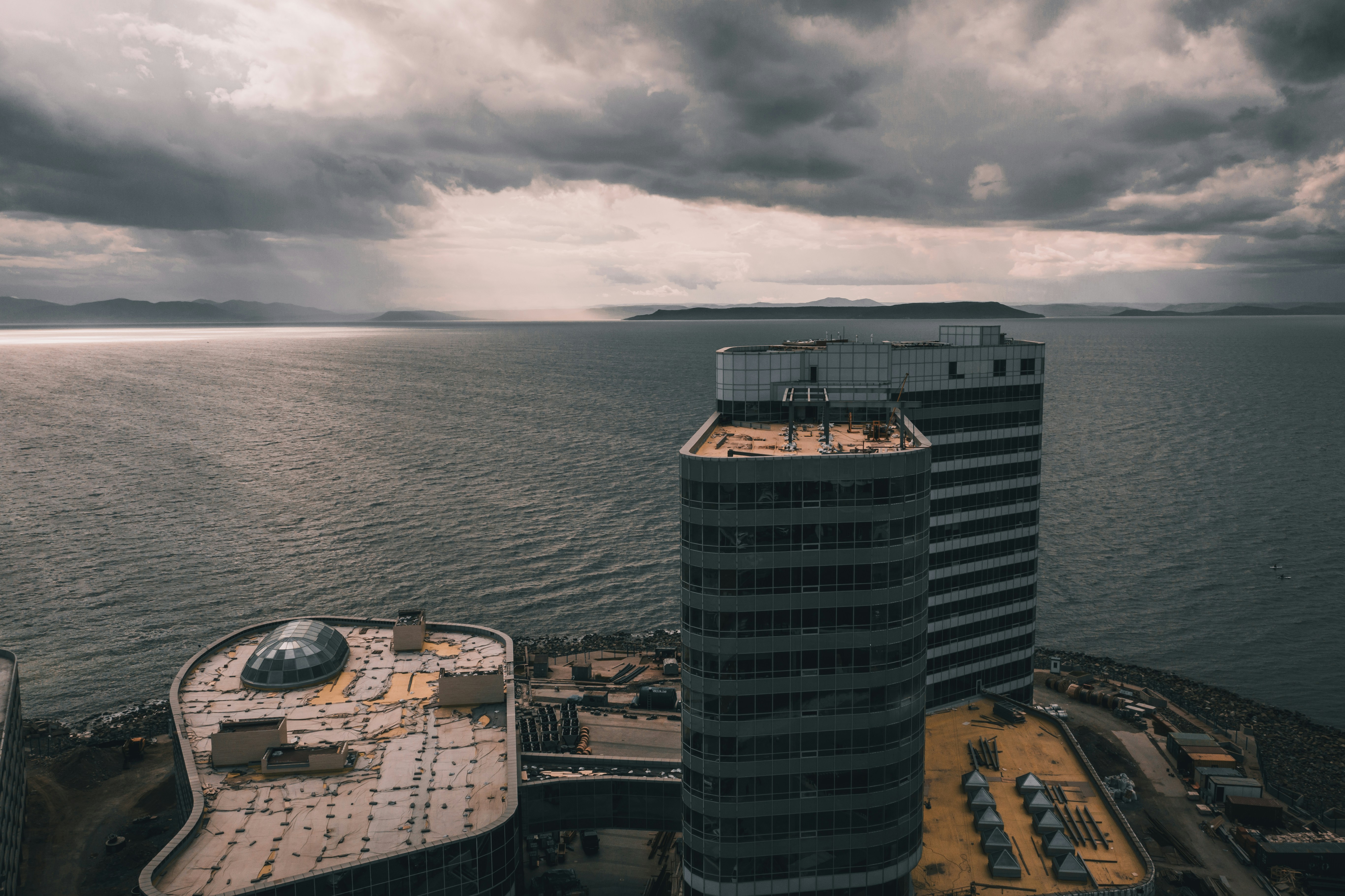 Modern buildings overlooking a vast body of water, with stormy clouds creating a moody atmosphere.