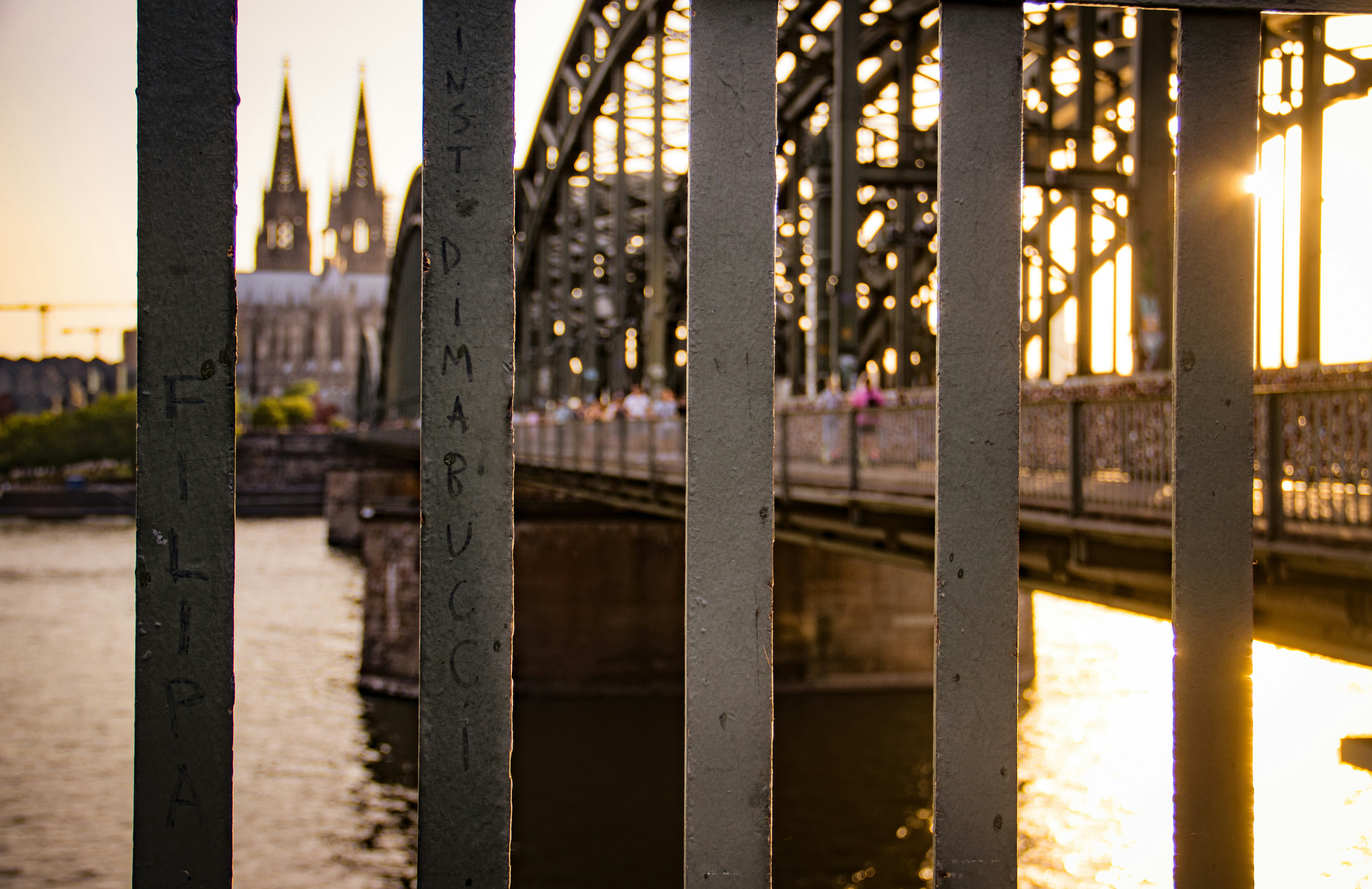 Sunset view of a cathedral framed by the bars of a bridge with warm light reflecting on the river.