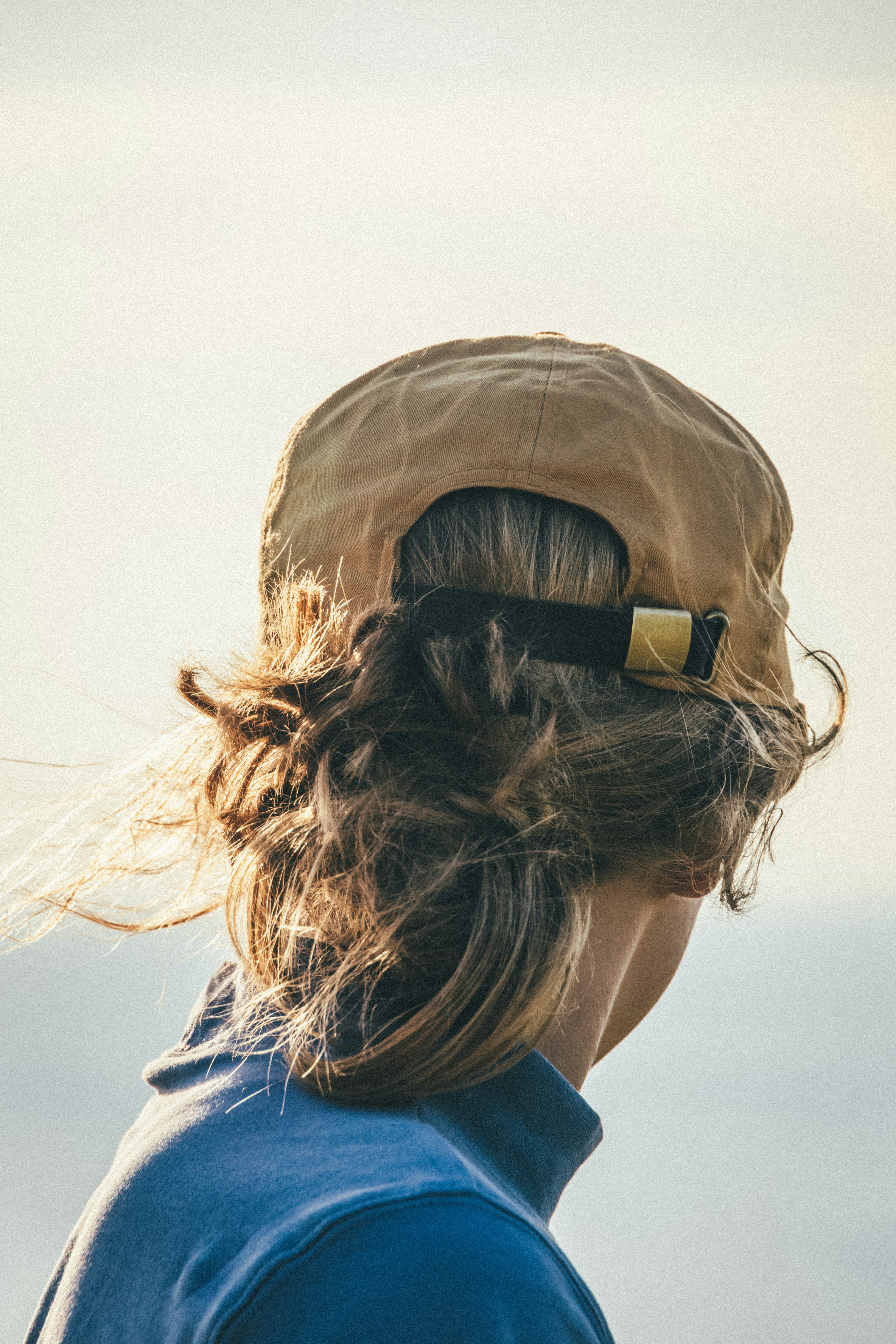 Wind-Tousled Back View of a Beachbound Traveler in a Tan Cap