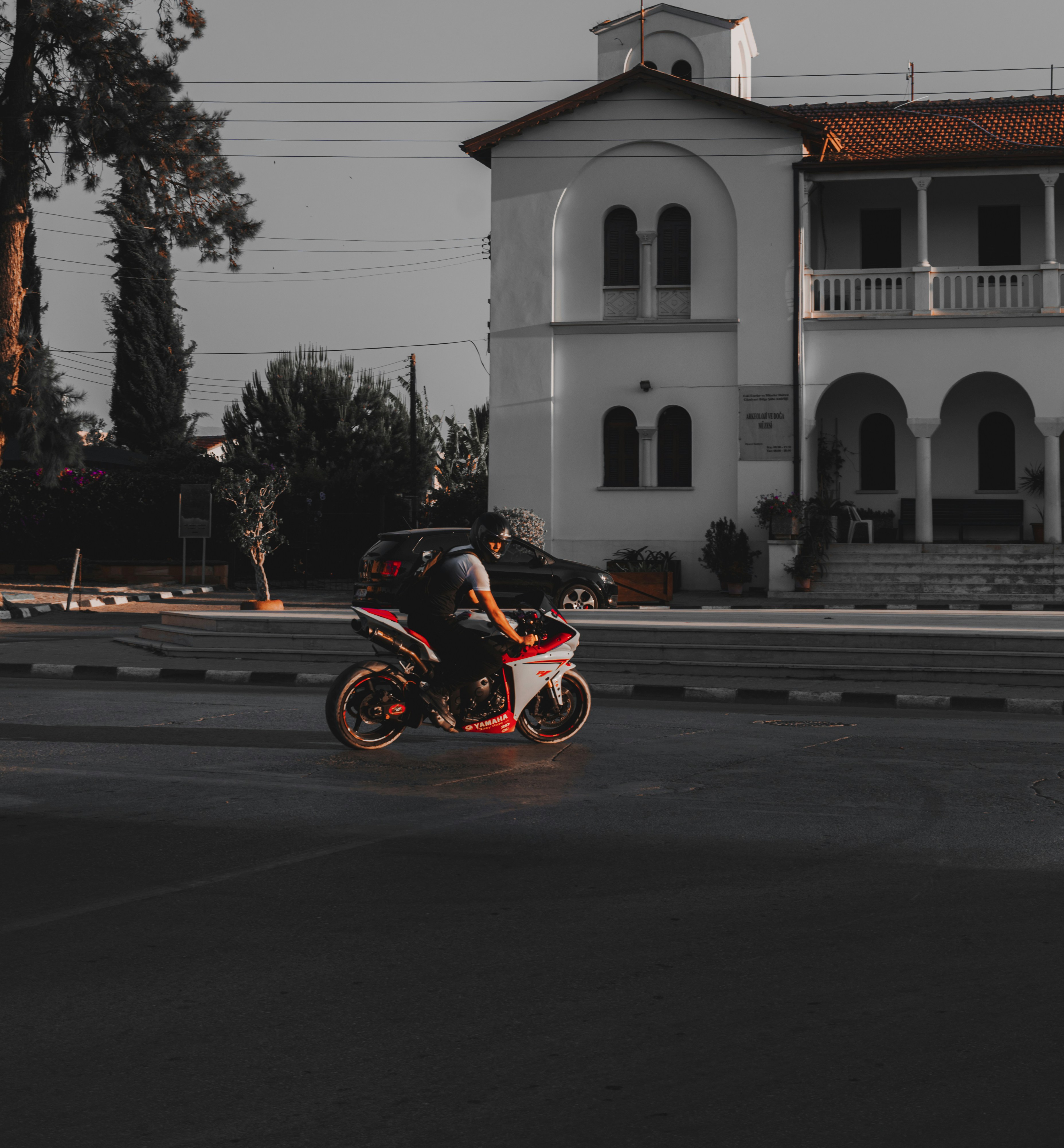 Man riding motorcycle on road near white concrete building during ...