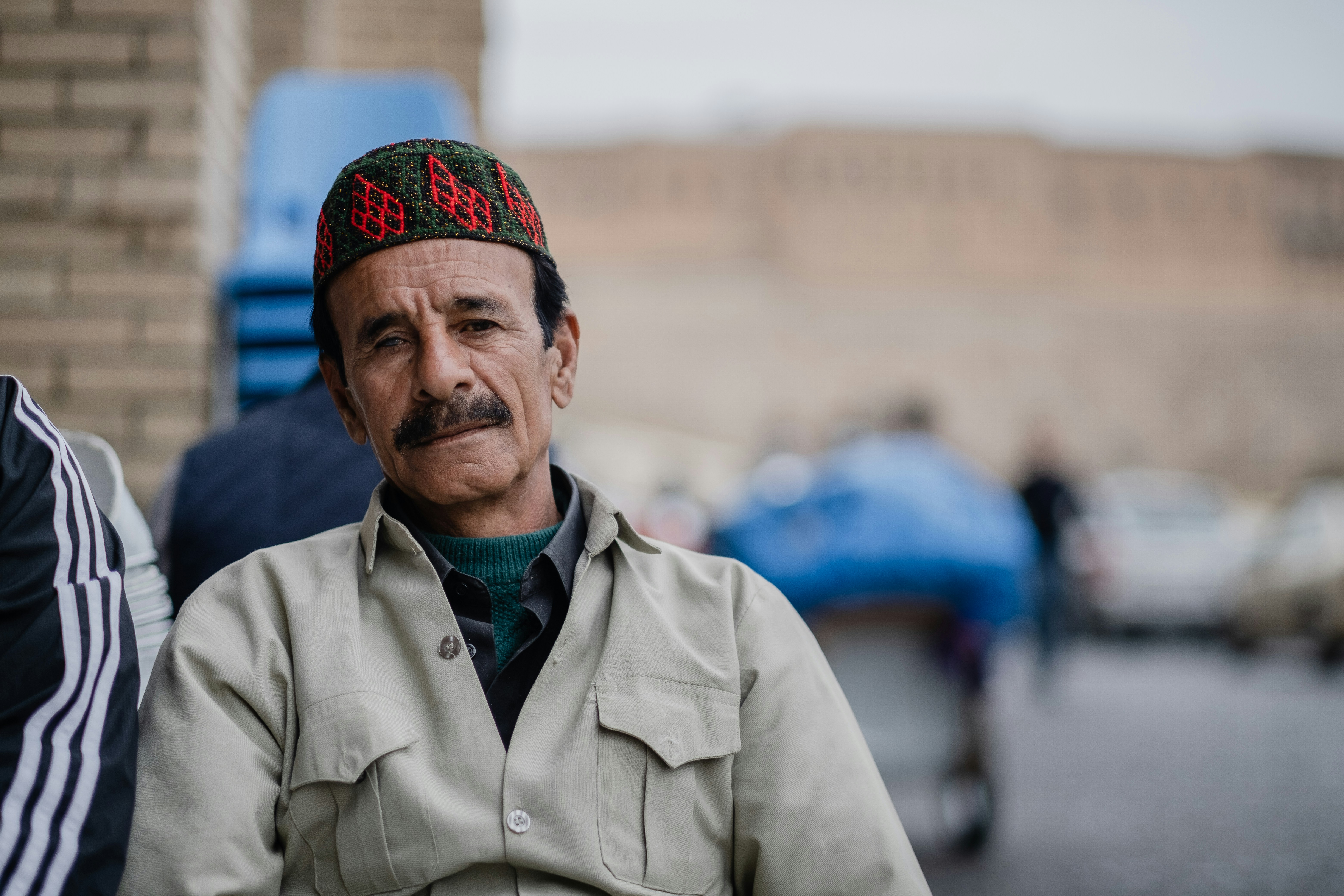 A gentleman in Kurdish clothes by the Citadel in Erbil. | man in gray button up shirt wearing blue and red knit cap