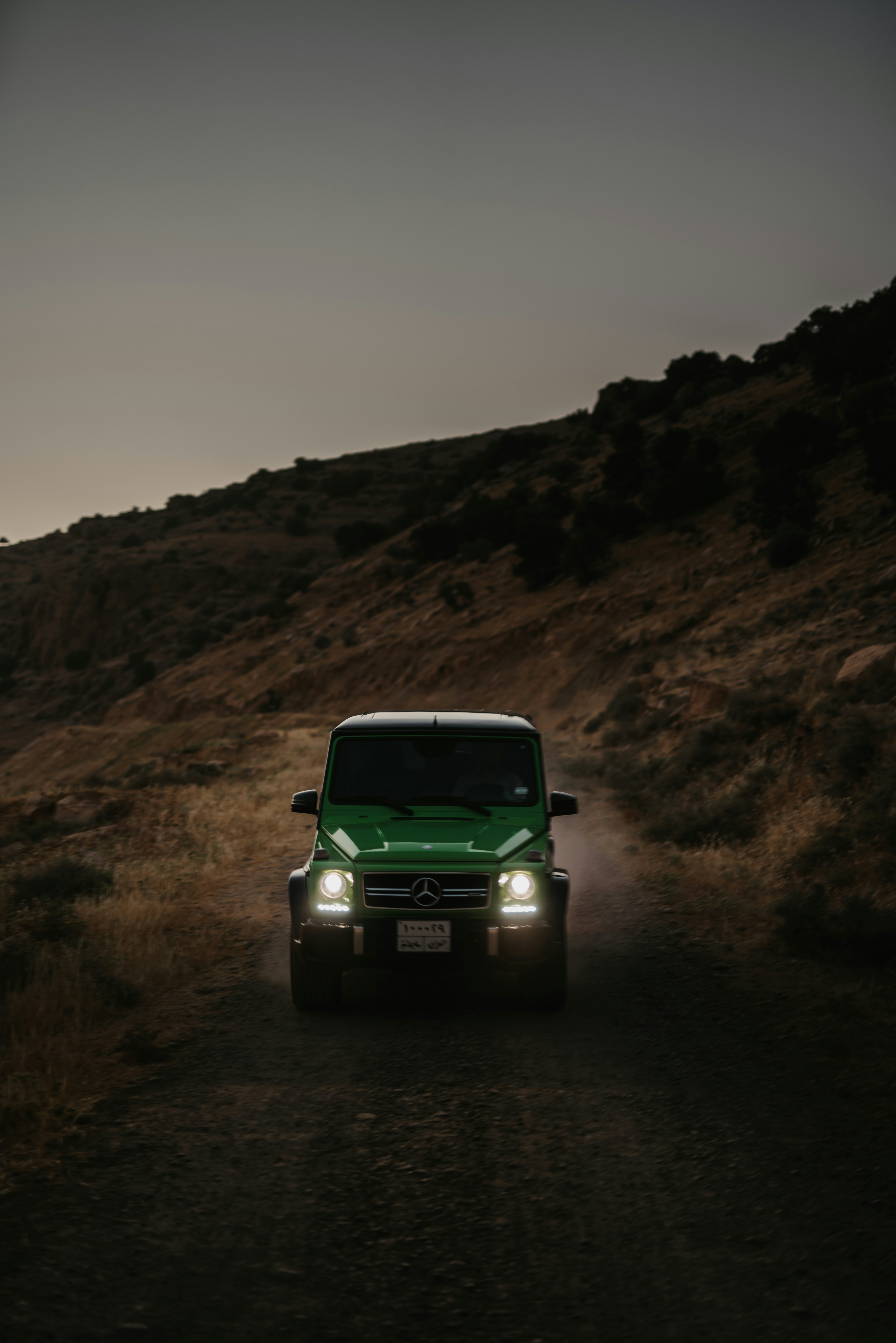 A striking green SUV navigates a rugged dirt path under a twilight sky, dust swirling in its wake.