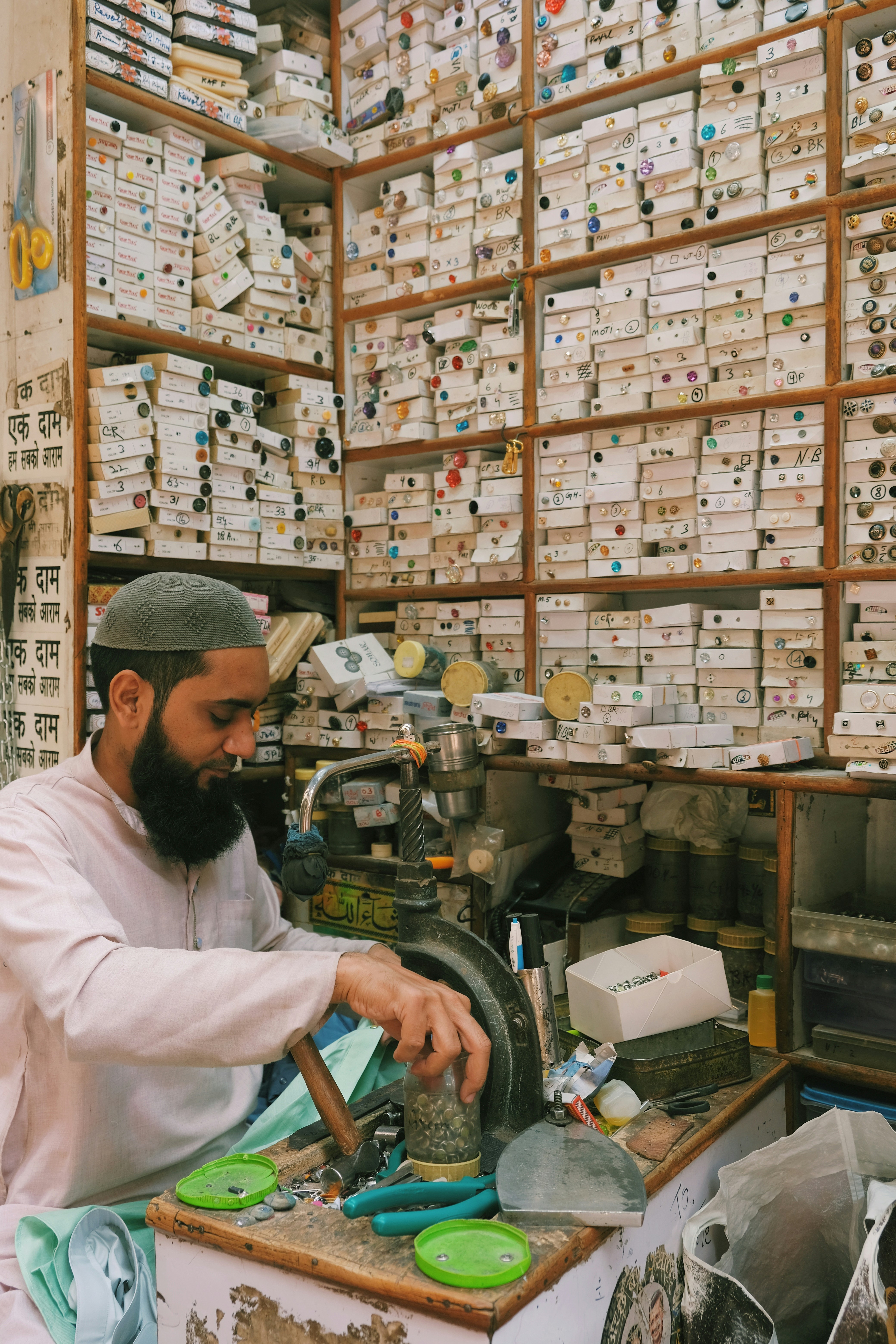 Bearded Artisan at a Metal Press Amid a Maze of Labeled Boxes