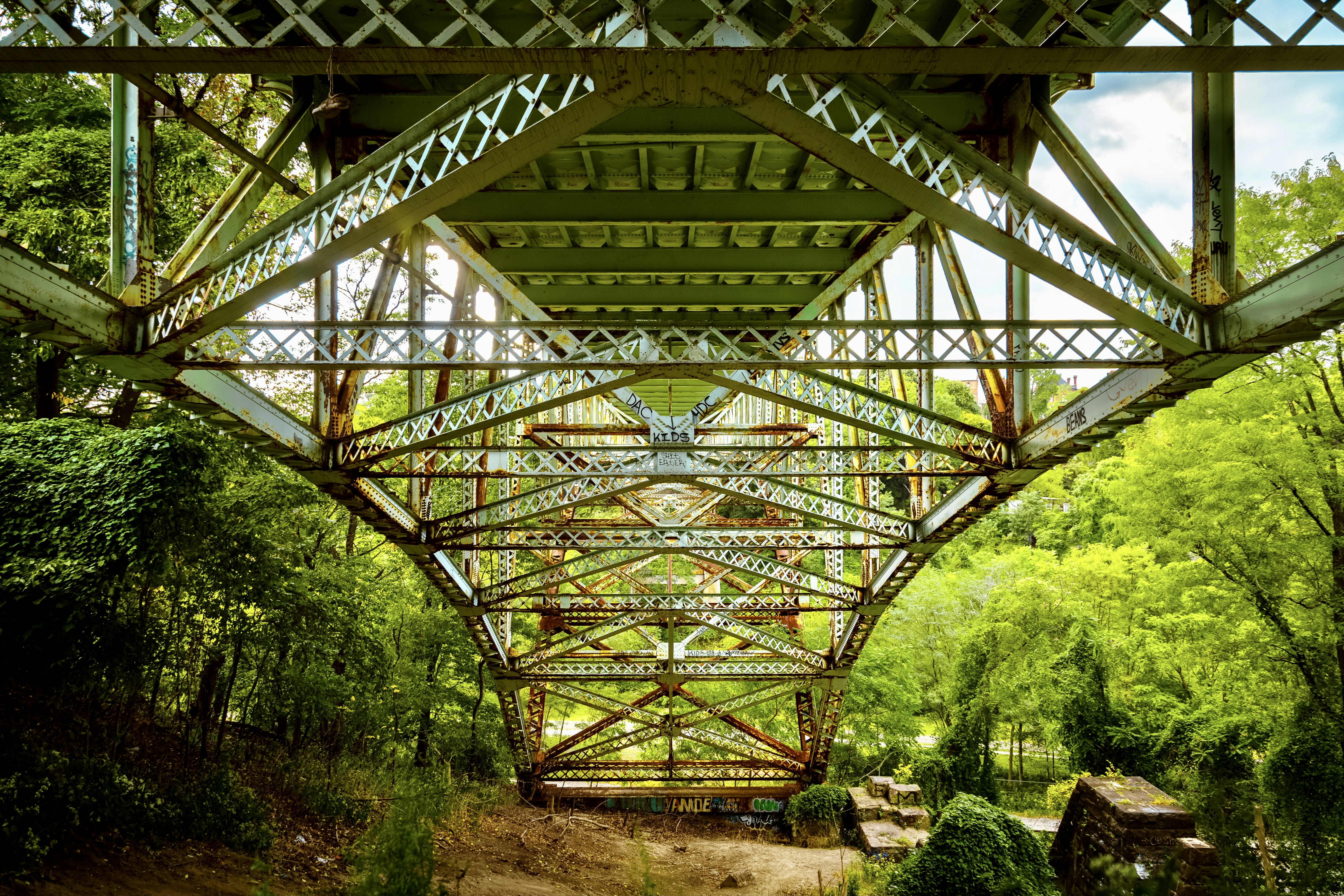 Underside view of a detailed metal bridge surrounded by lush green foliage.