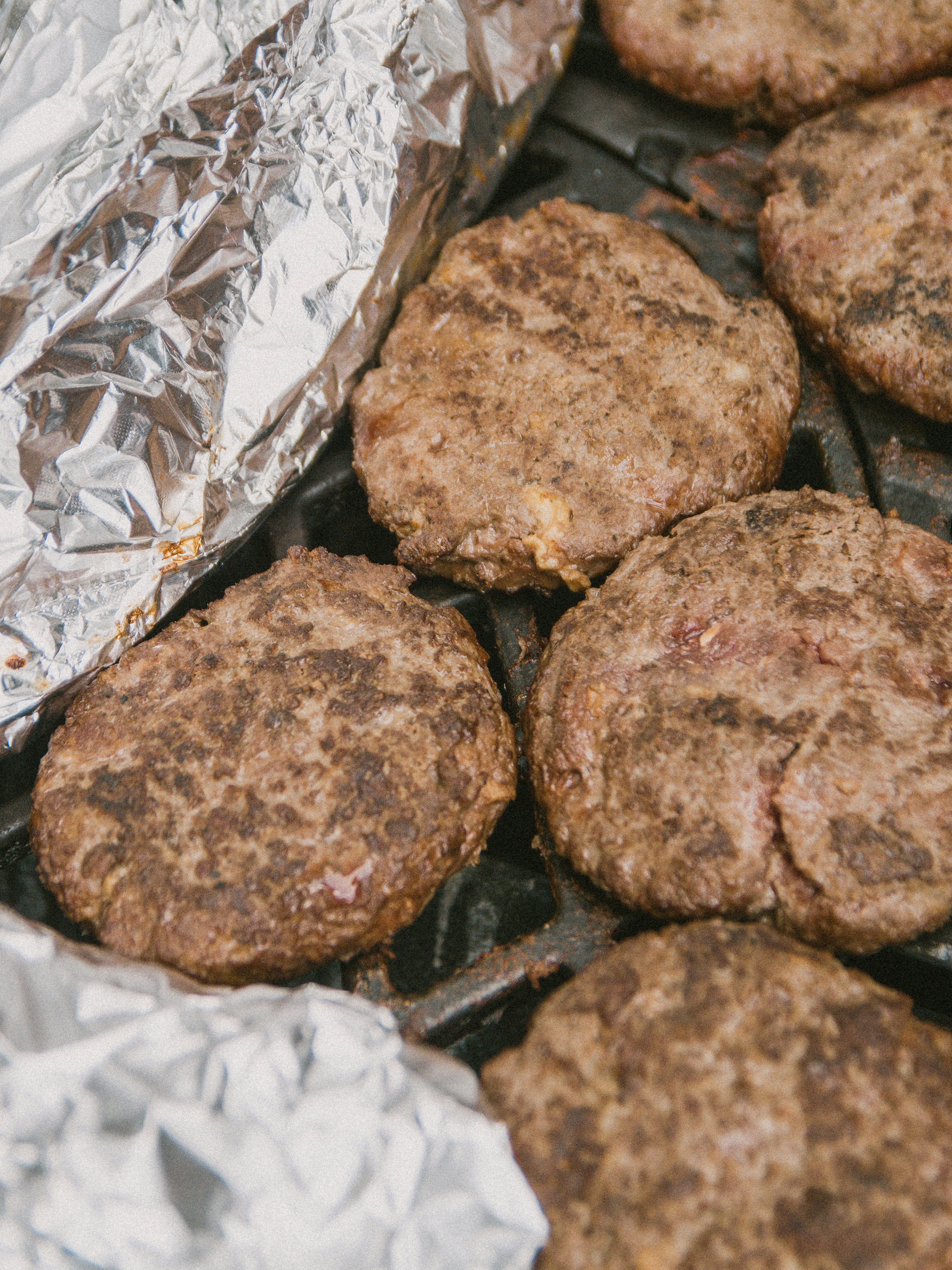 Charred Edges on a Grill: Close-Up Patties Amid Foil