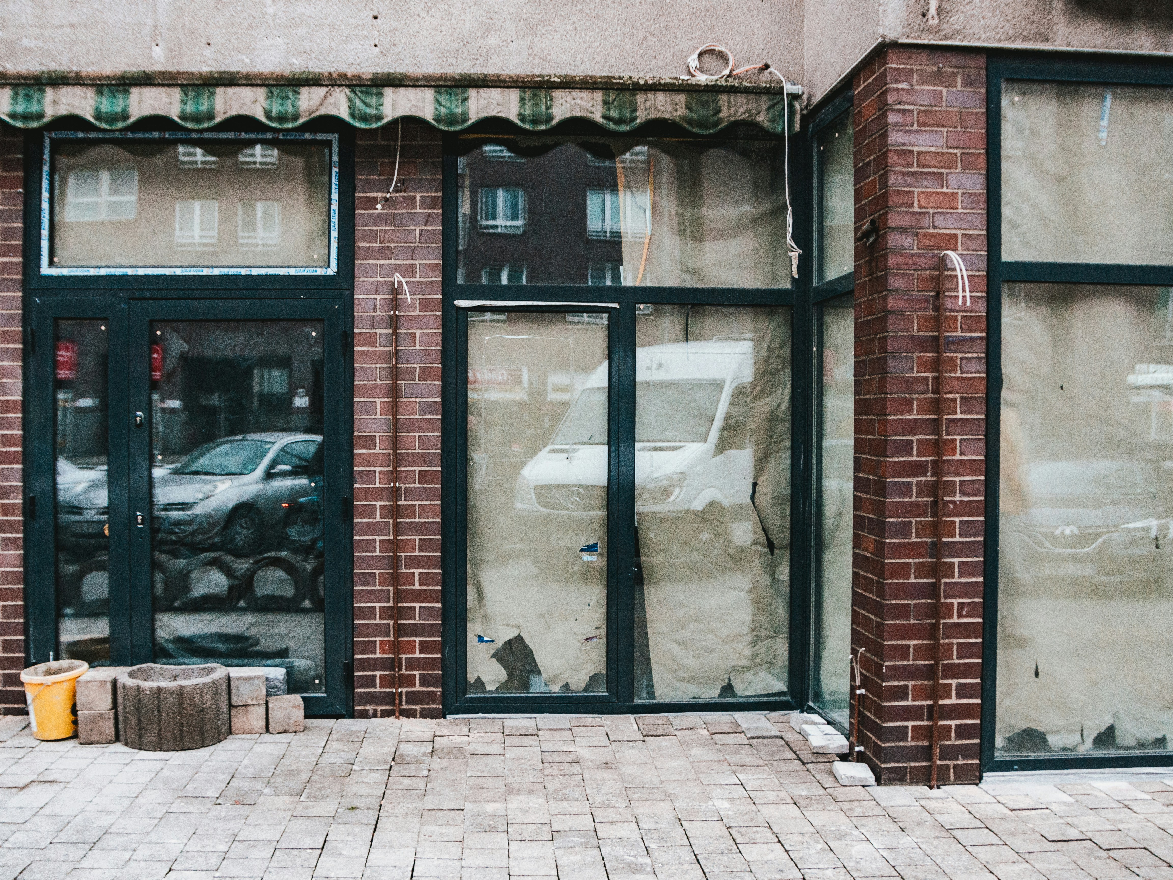 Storefront with brick walls and large windows reflecting a parked van and street scene.