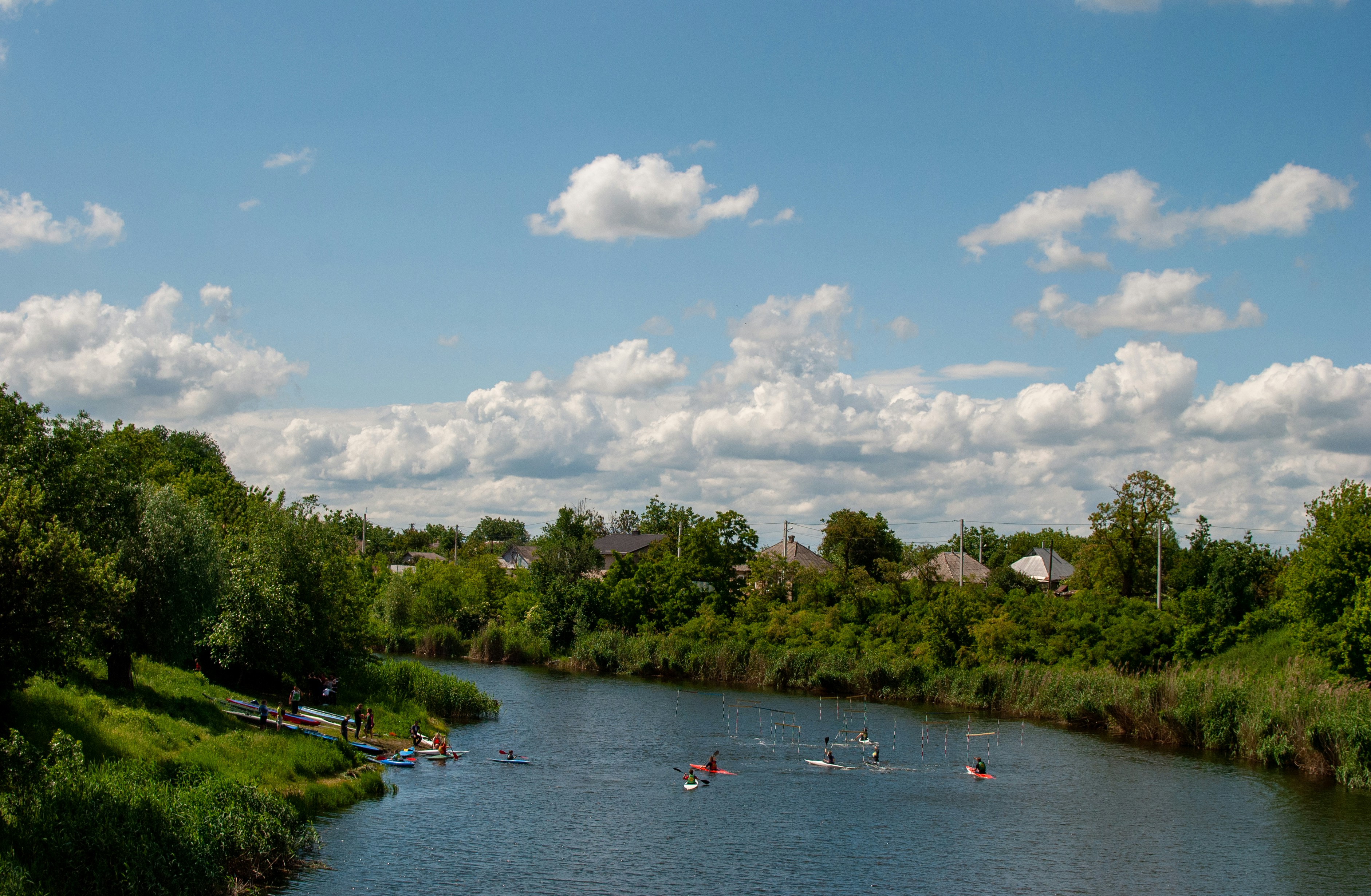 Kayakers navigate a tranquil river surrounded by lush greenery and a vibrant sky filled with clouds.