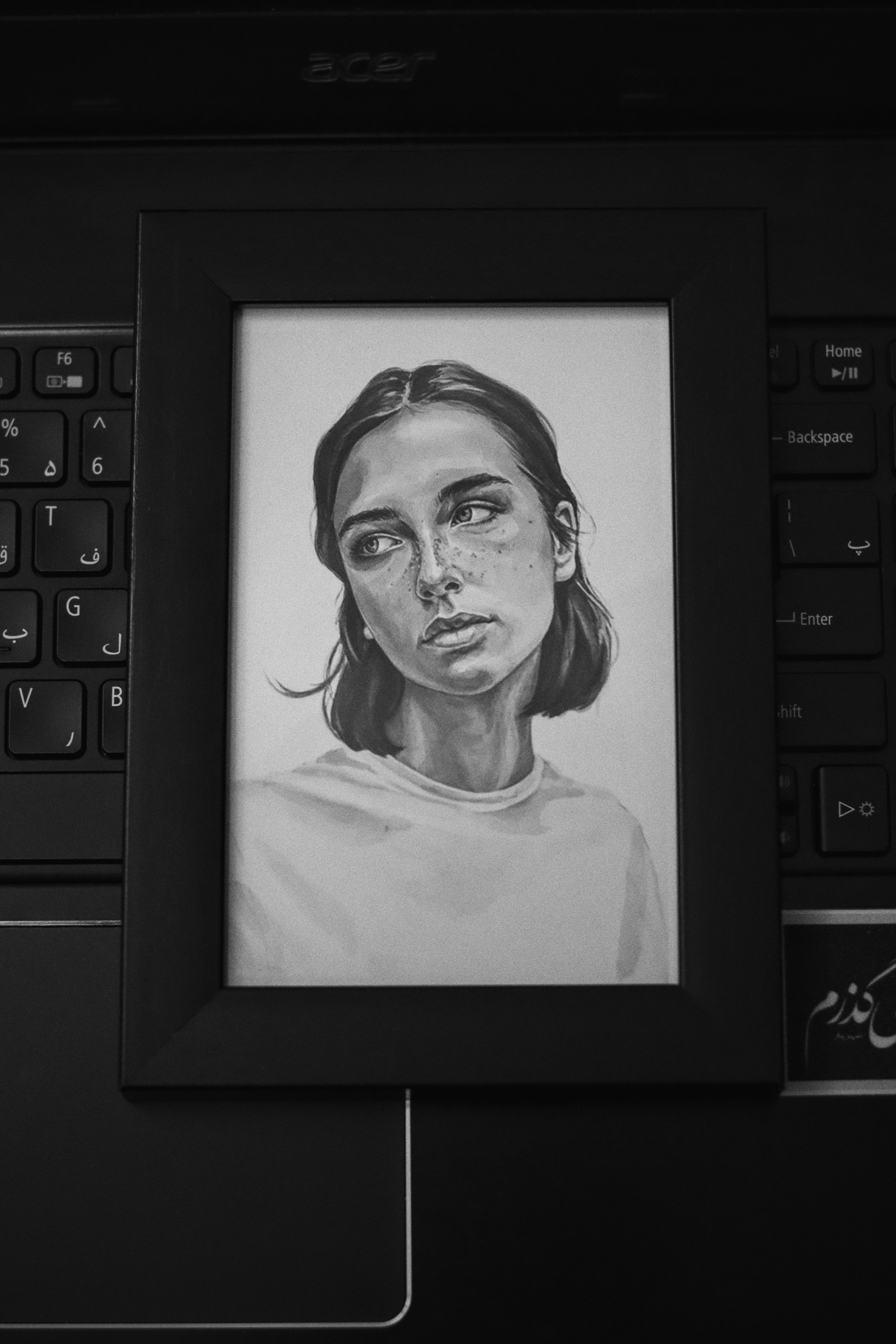 Black and white portrait illustration of a young woman with a thoughtful expression, framed and placed on a laptop keyboard.