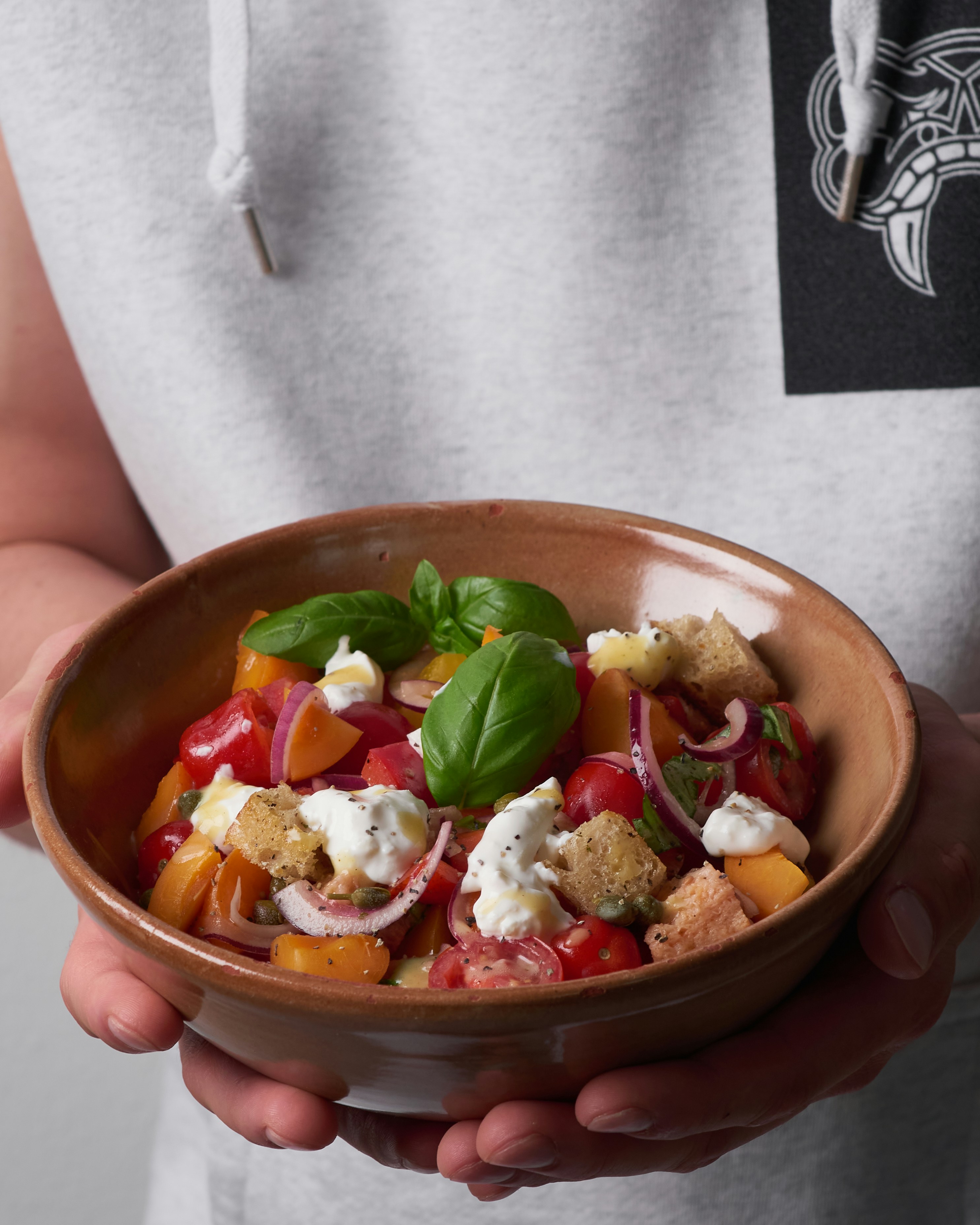 Rainbow Harvest in a Clay Bowl: Basil-Topped Veggie Salad Held by Warm Hands