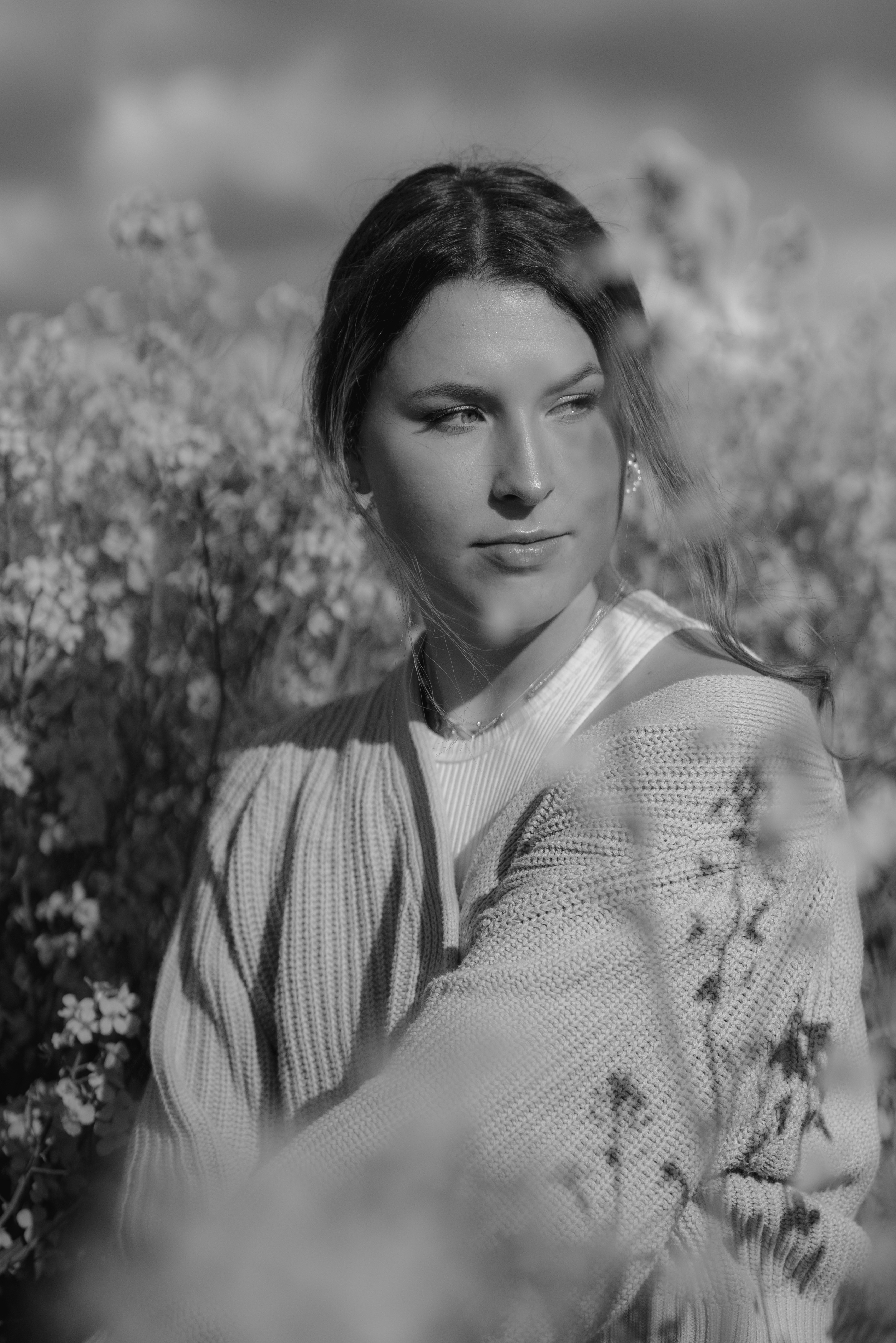 A woman gazes thoughtfully amidst a field of delicate flowers, embodying a serene connection to nature in monochrome.