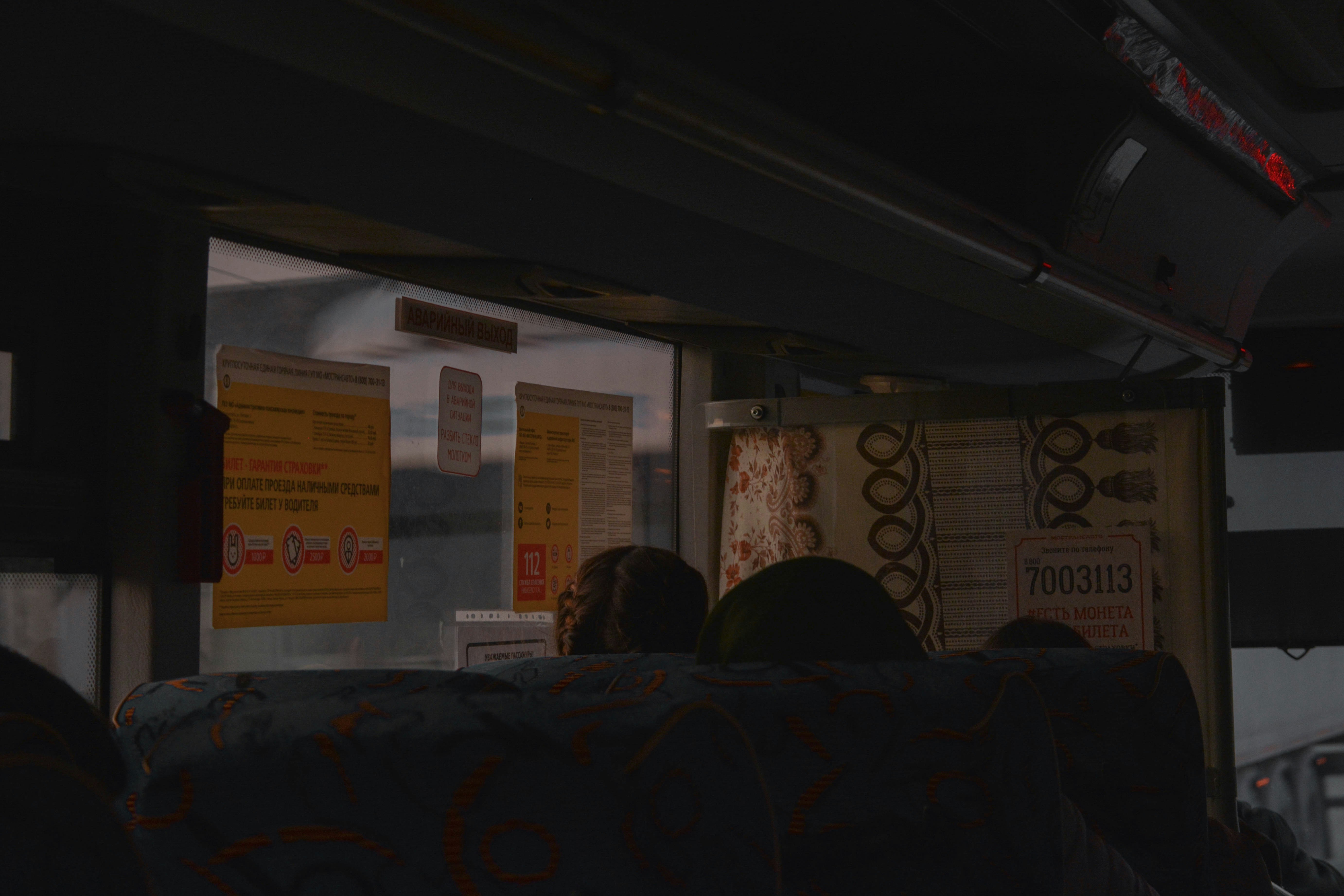 Interior view of a bus showcasing passengers and transit information displayed on the window. The atmosphere hints at a late evening commute.