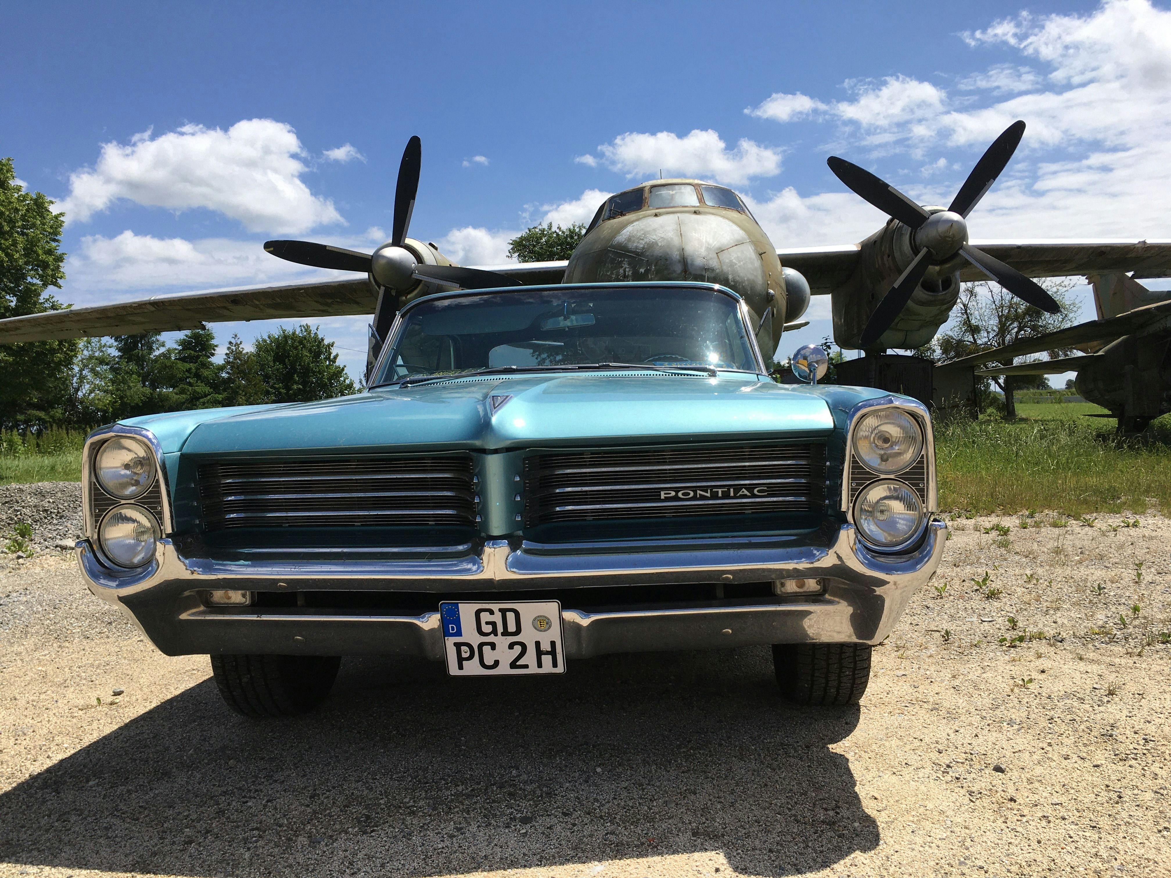 Front-View of a Classic Turquoise Pontiac with Propeller Aircraft Backdrop