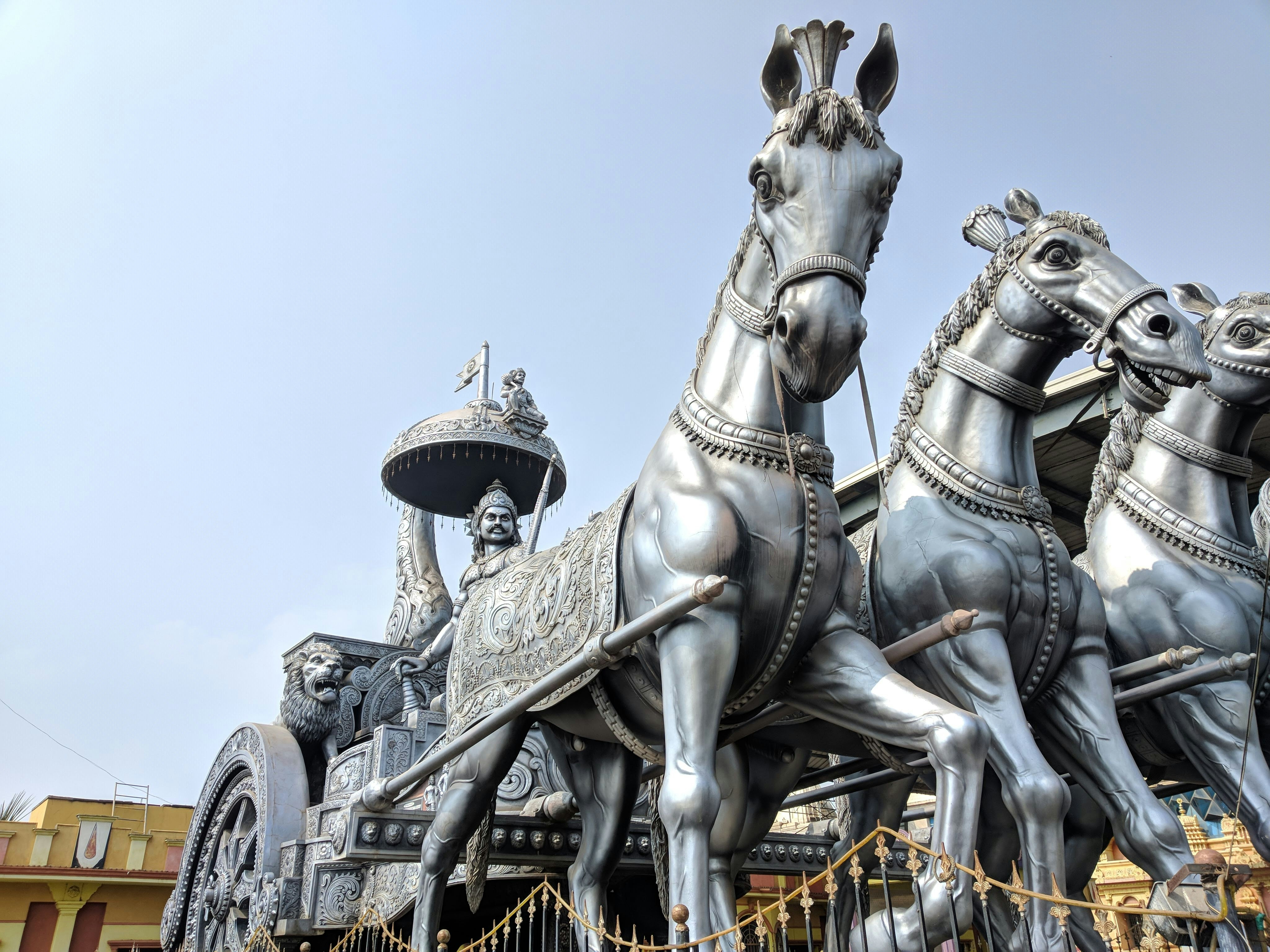 Ornate statue of a chariot drawn by three horses with a warrior holding a parasol.