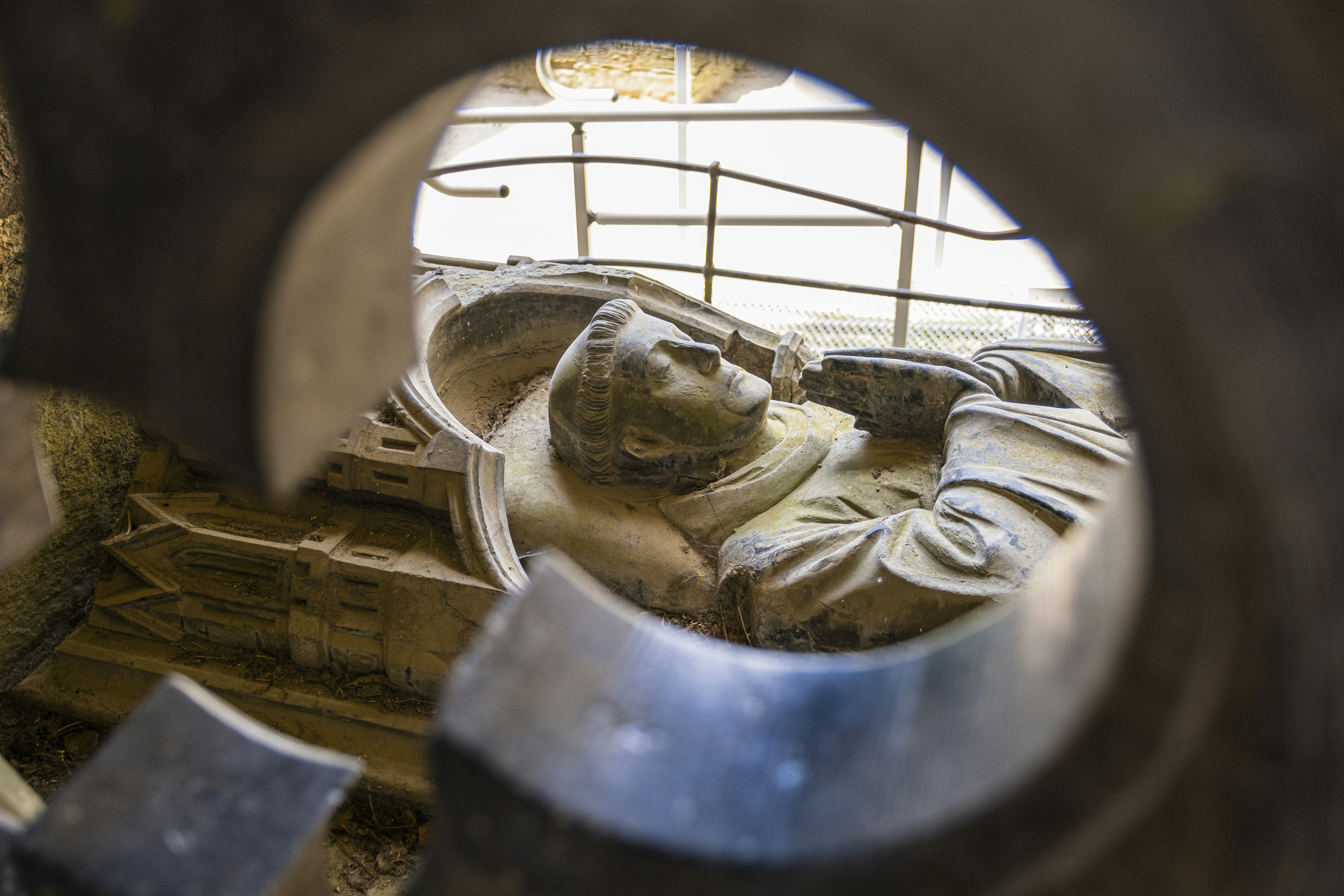 Intricate stone sculpture of a figure, partially obscured by a circular framing element, revealing a glimpse of its detailed craftsmanship.