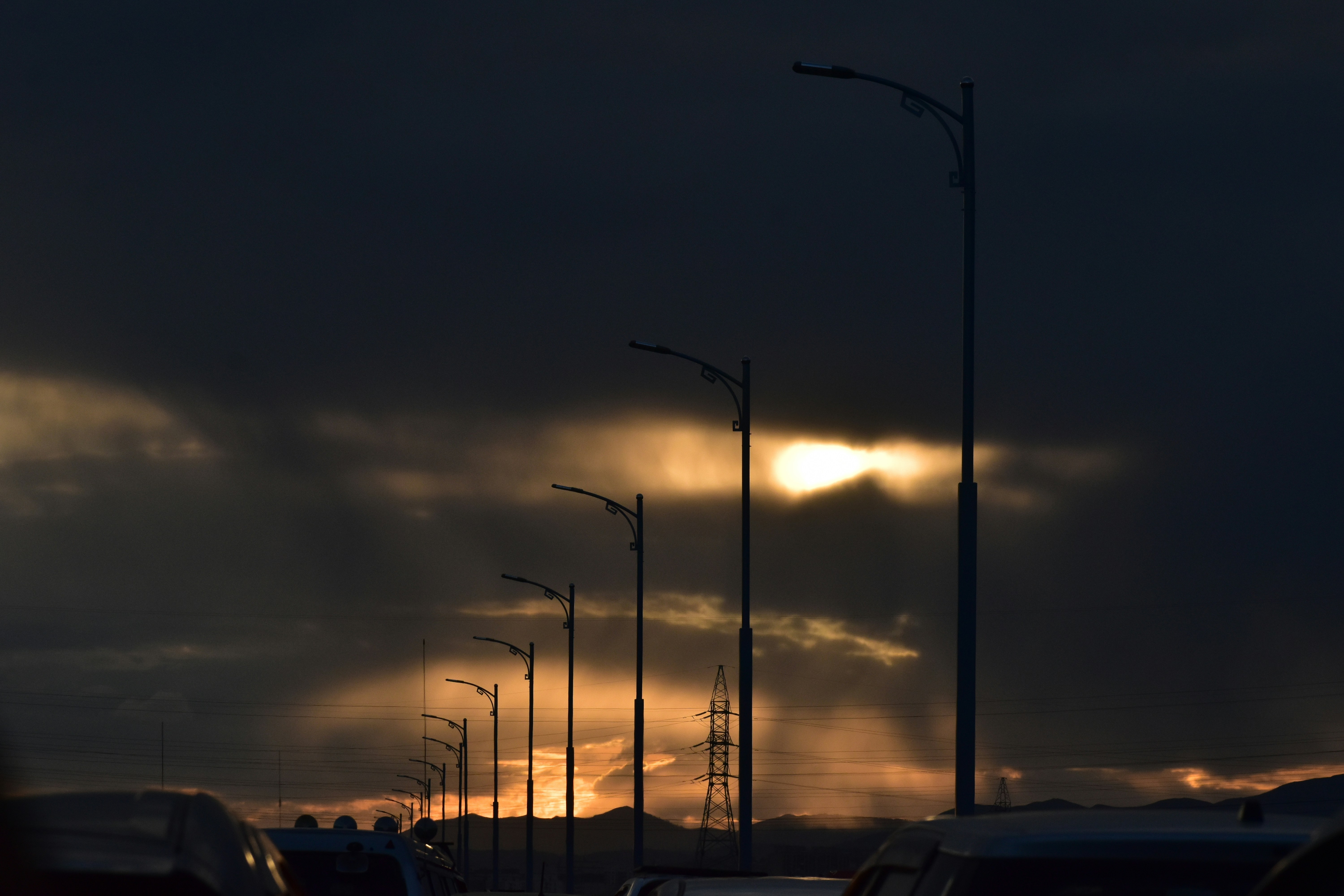 Streetlights and distant vehicles silhouetted against a dramatic sunset sky with scattered clouds.