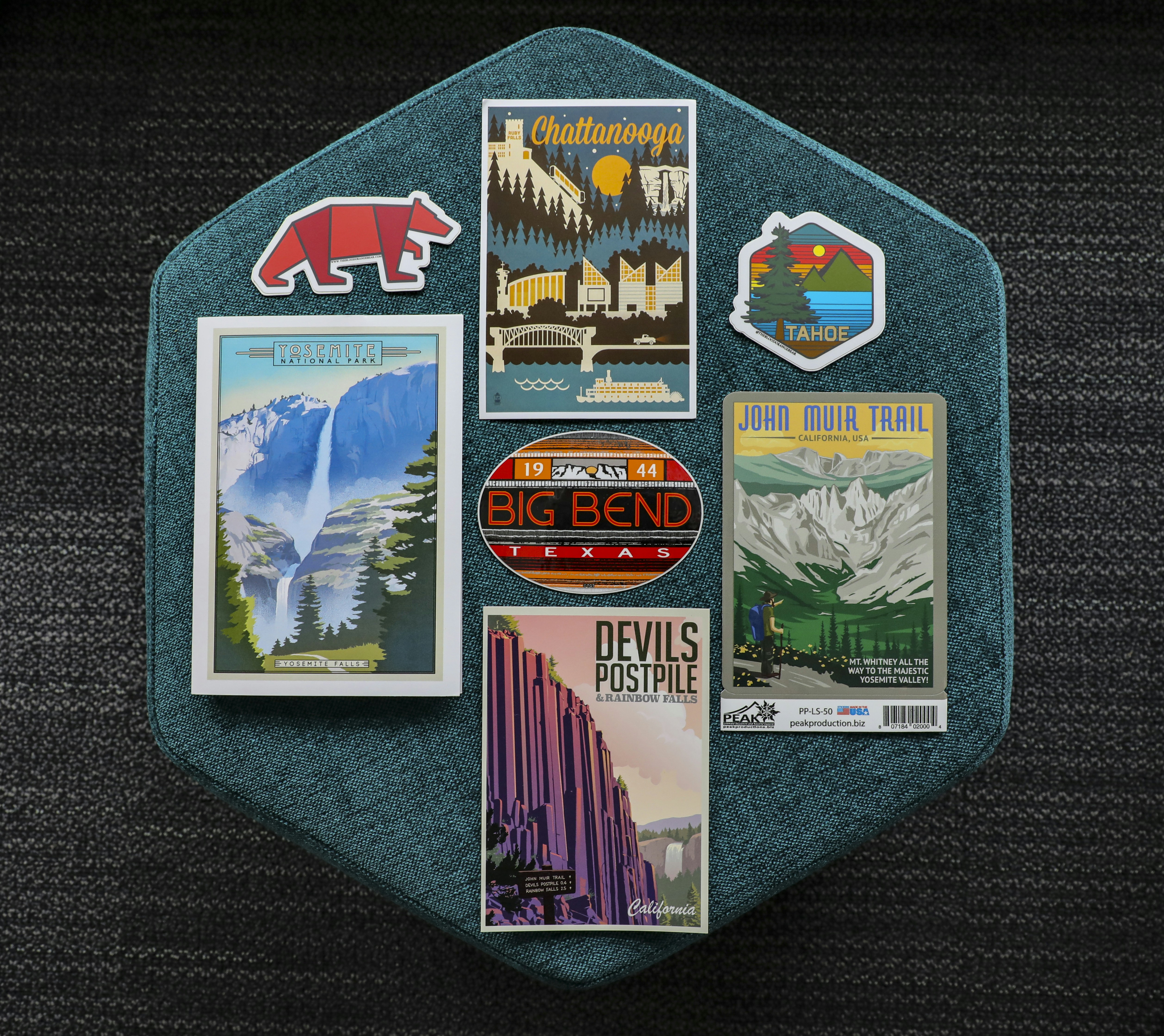 A collection of vibrant travel stickers showcasing iconic American destinations, arranged on a textured teal surface.