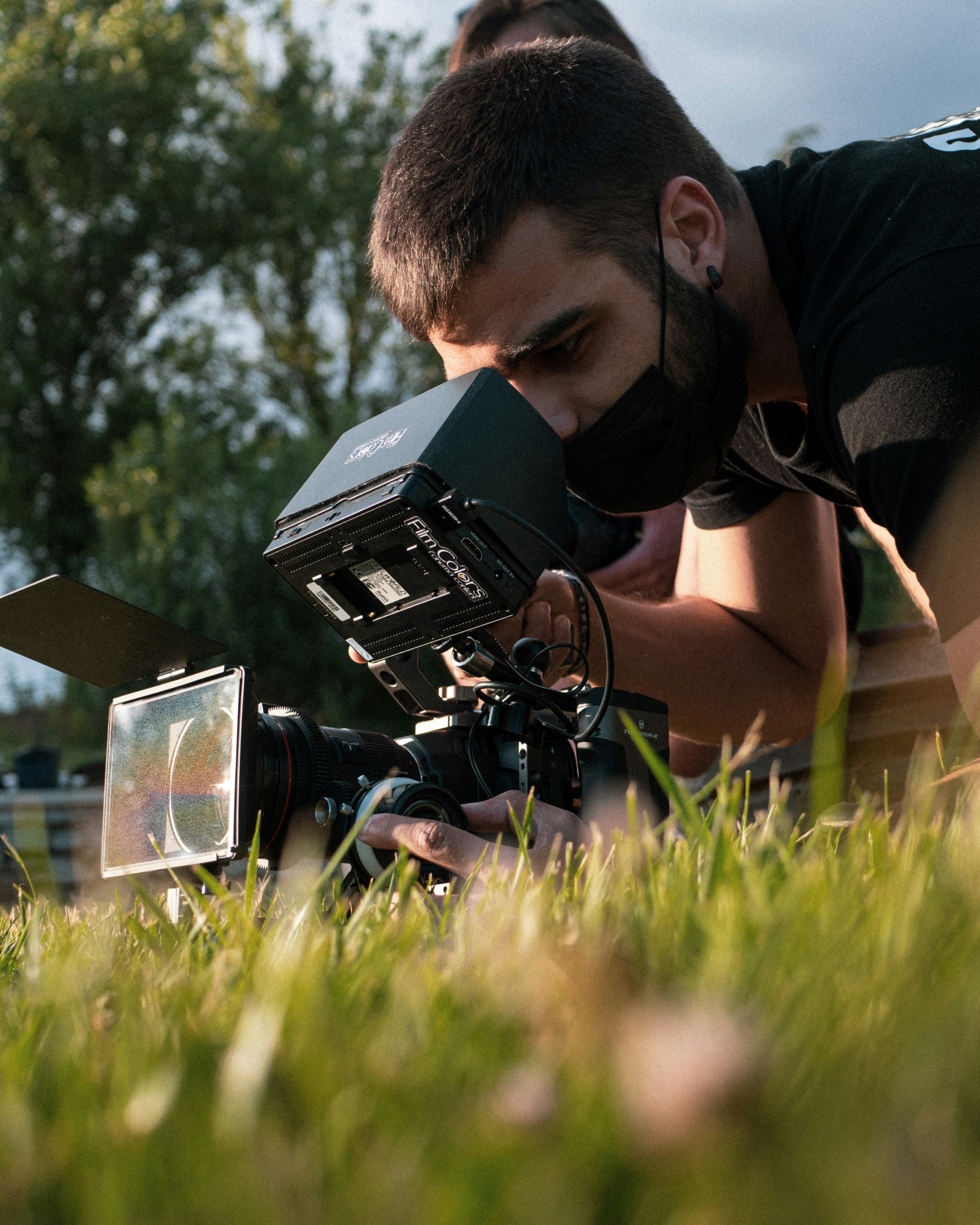 Man in black shirt and black sunglasses holding black camera on green ...