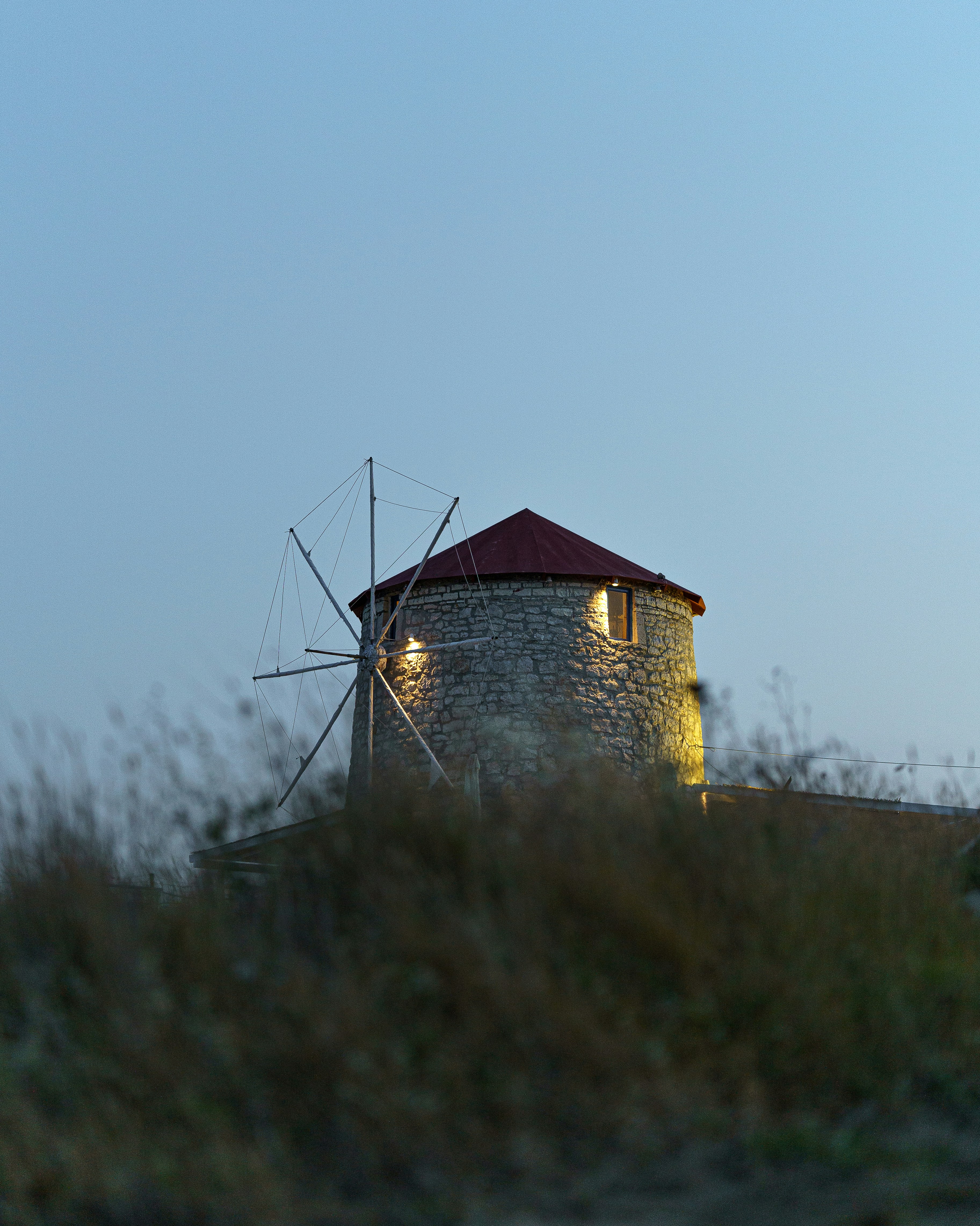 A vintage windmill stands against a twilight sky, illuminated by soft lights, showcasing its rustic charm and historical significance.
