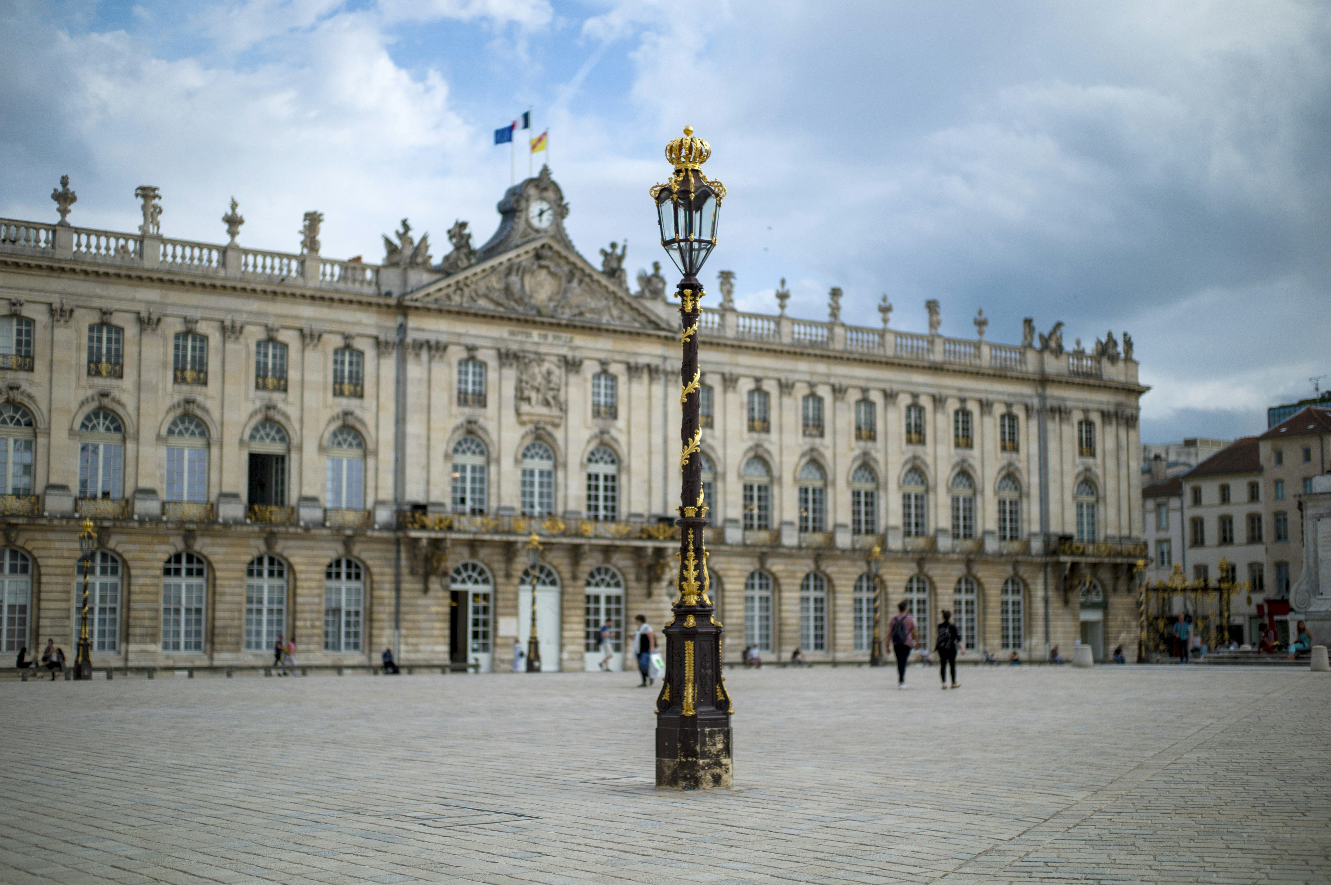 Intricate street lamp set against the backdrop of an ornate historical building under a cloudy sky.