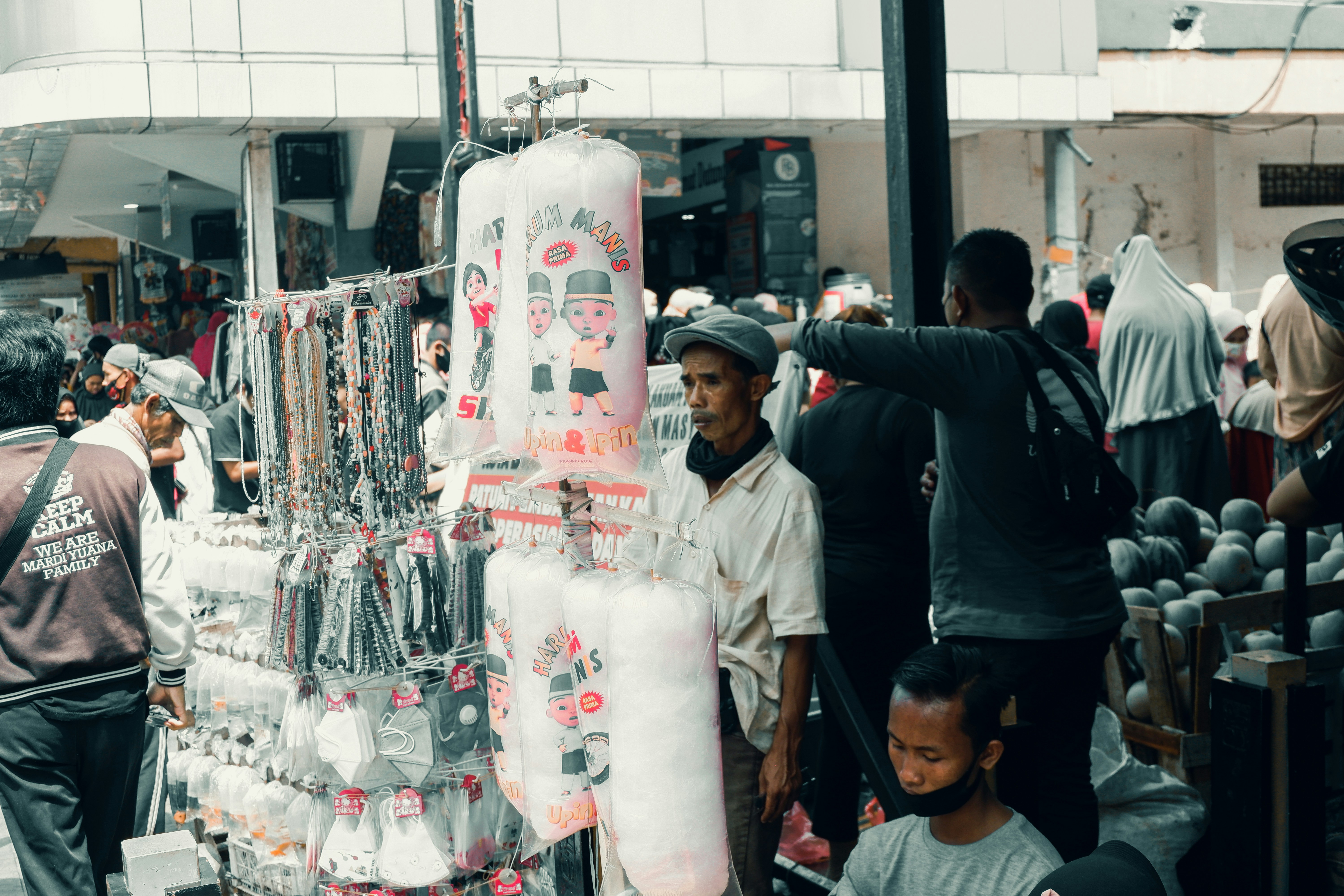 Vendors display colorful goods on a busy urban street under bright daylight.