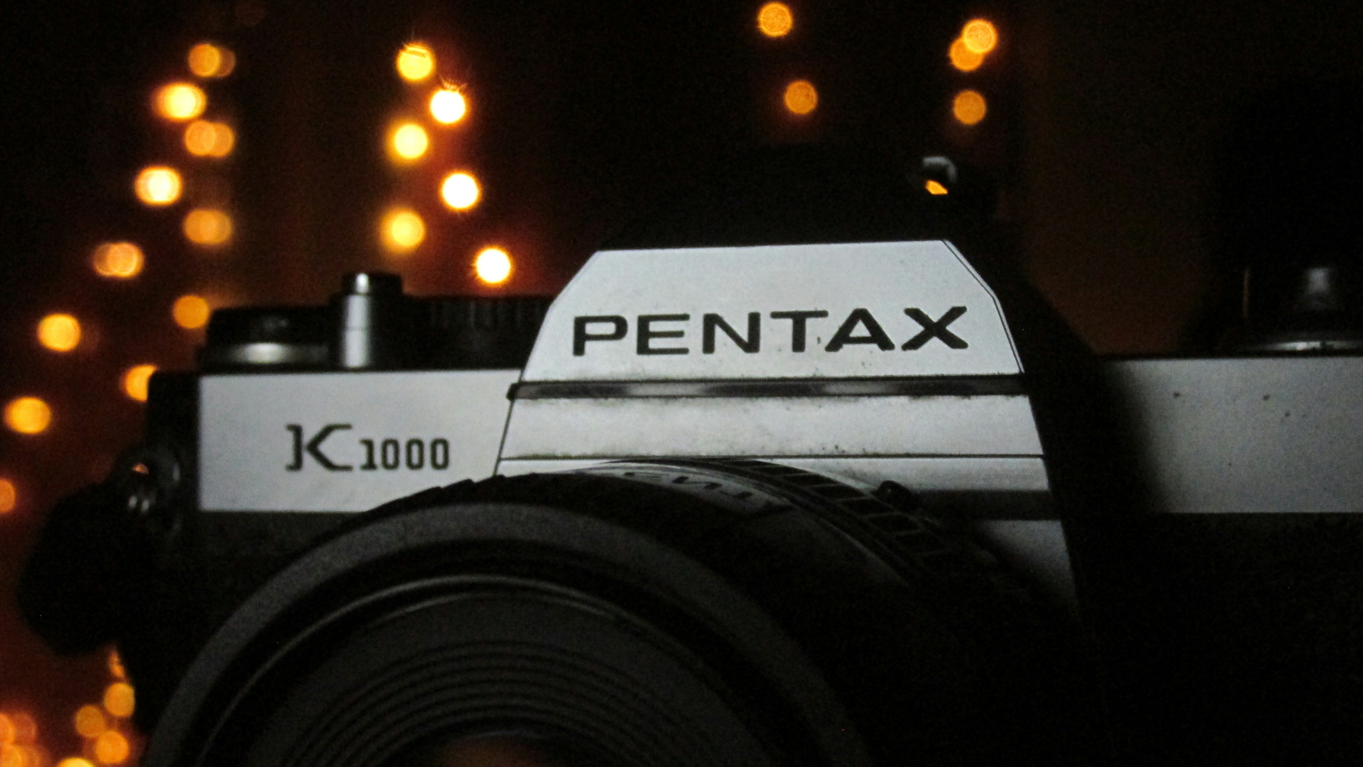 Close-up of a Pentax K1000 camera against a backdrop of soft, glowing bokeh lights.