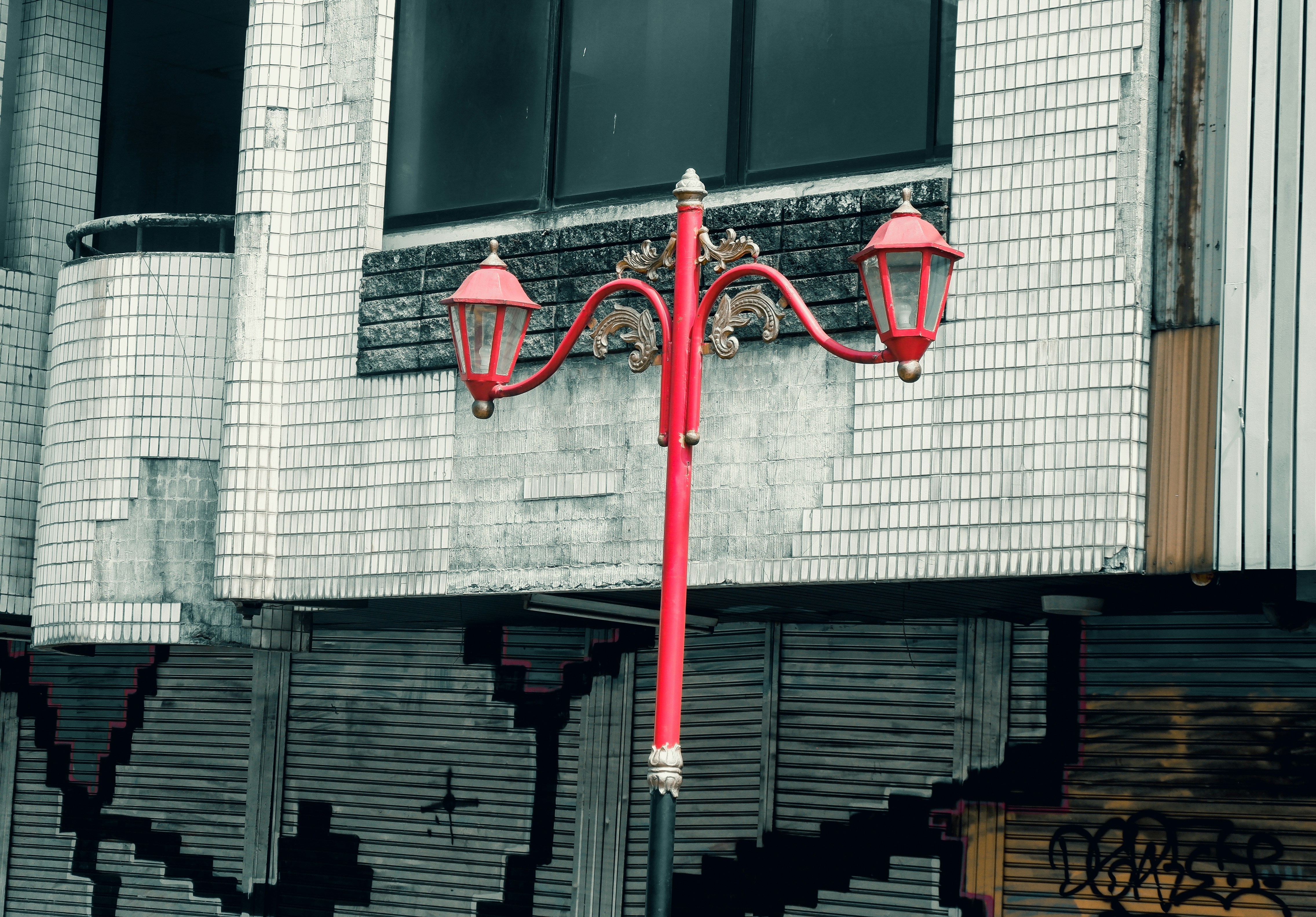 Vintage red street lamp stands against a backdrop of weathered tiles and graffiti, highlighting urban decay and color contrast.