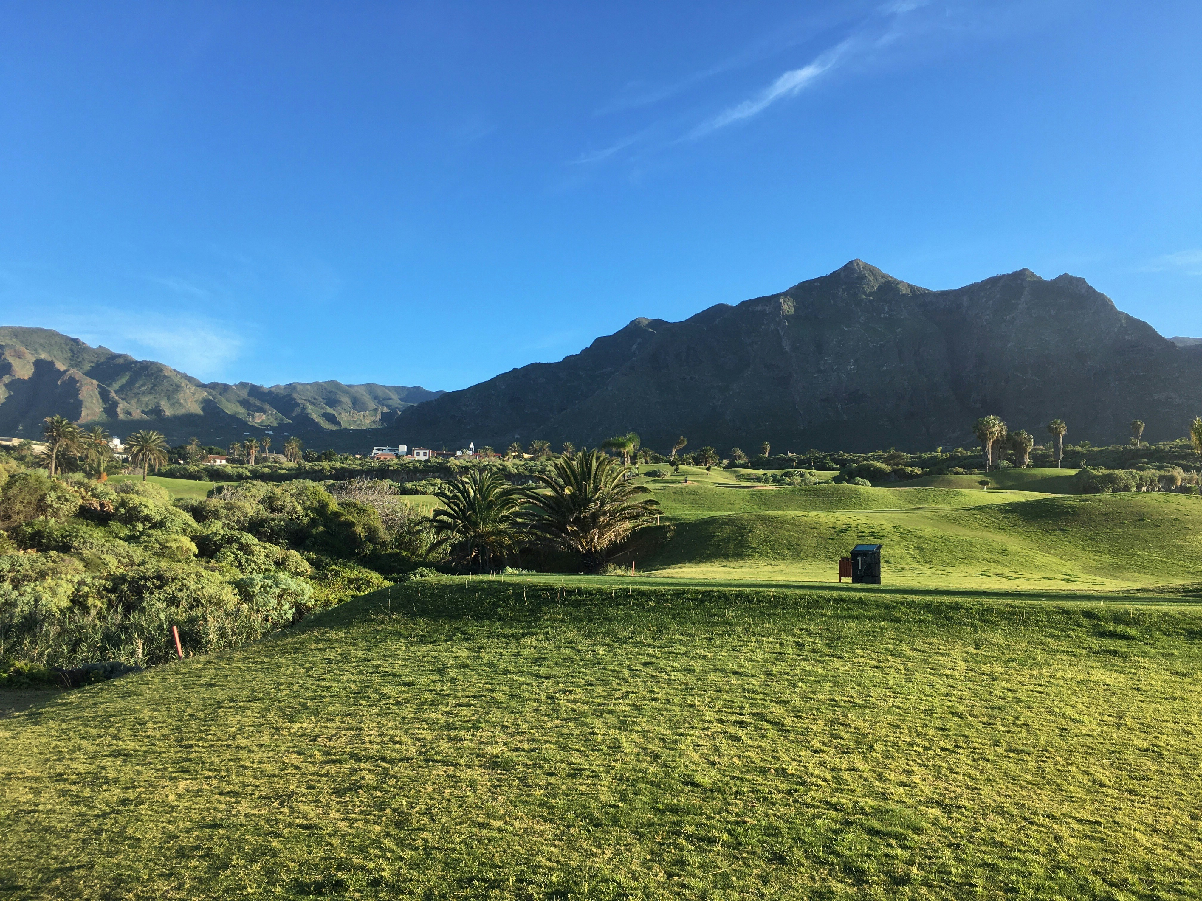 Expansive golf course landscape featuring lush greenery and distant mountains under a clear blue sky.