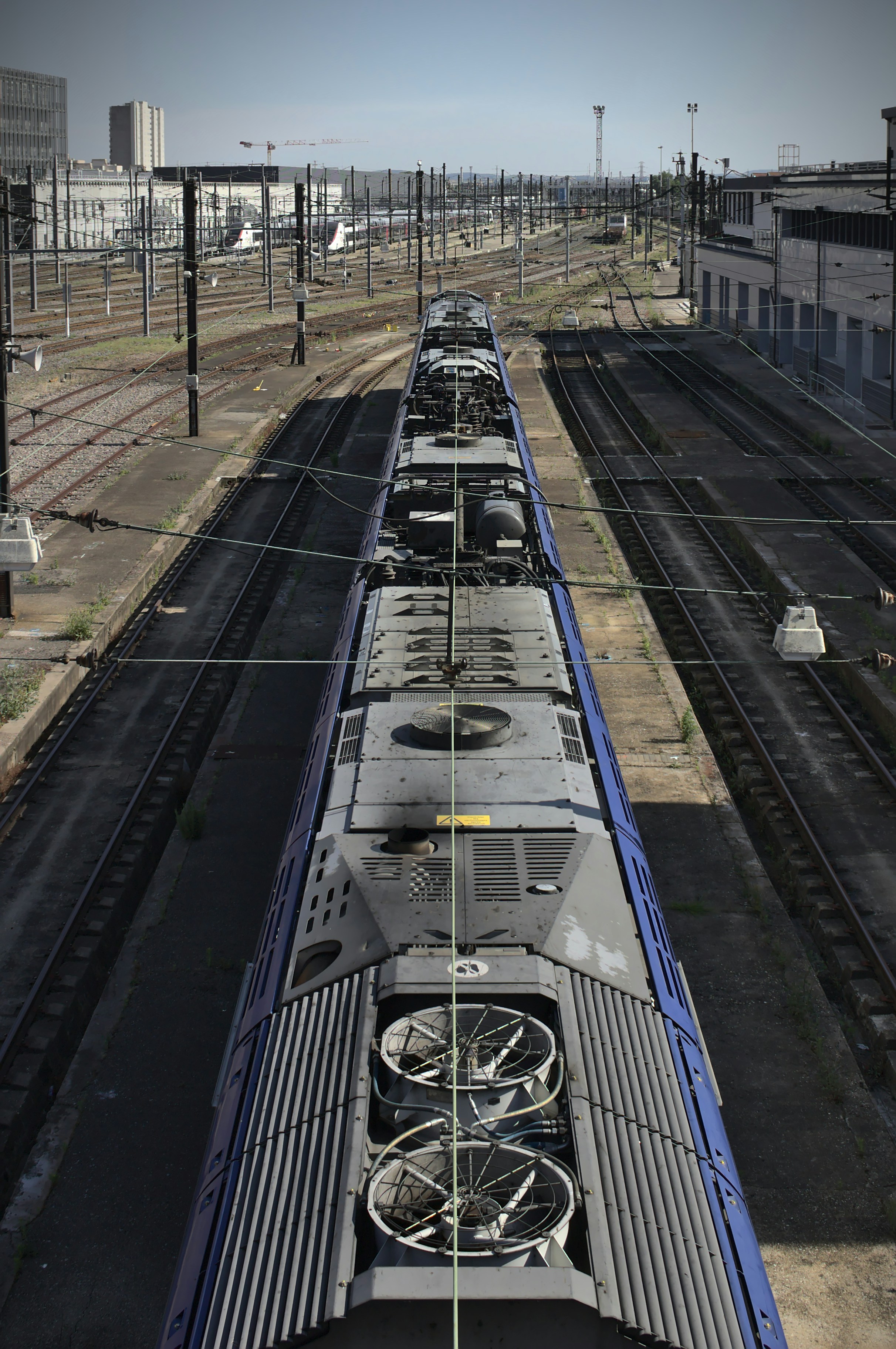 Aerial view of a stationary train with visible ventilation systems, surrounded by railway tracks and industrial structures.