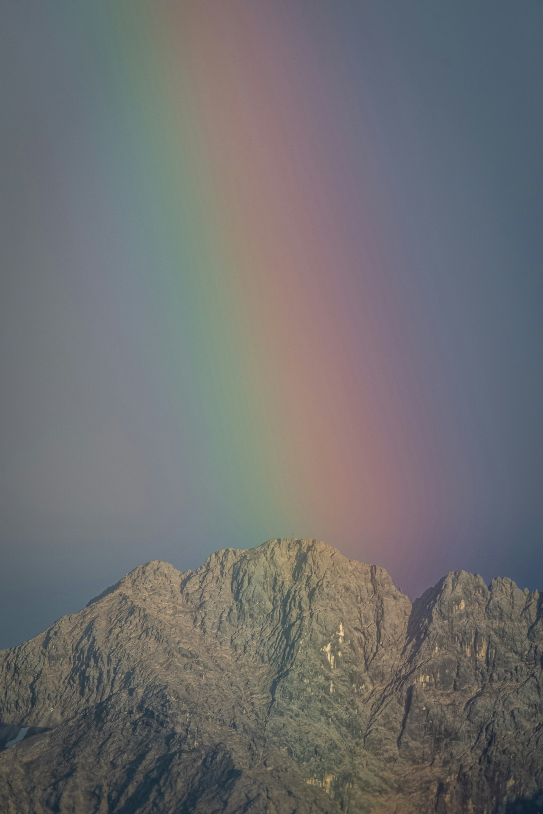 A vibrant rainbow arches gracefully over rugged mountain tops under a clear sky.