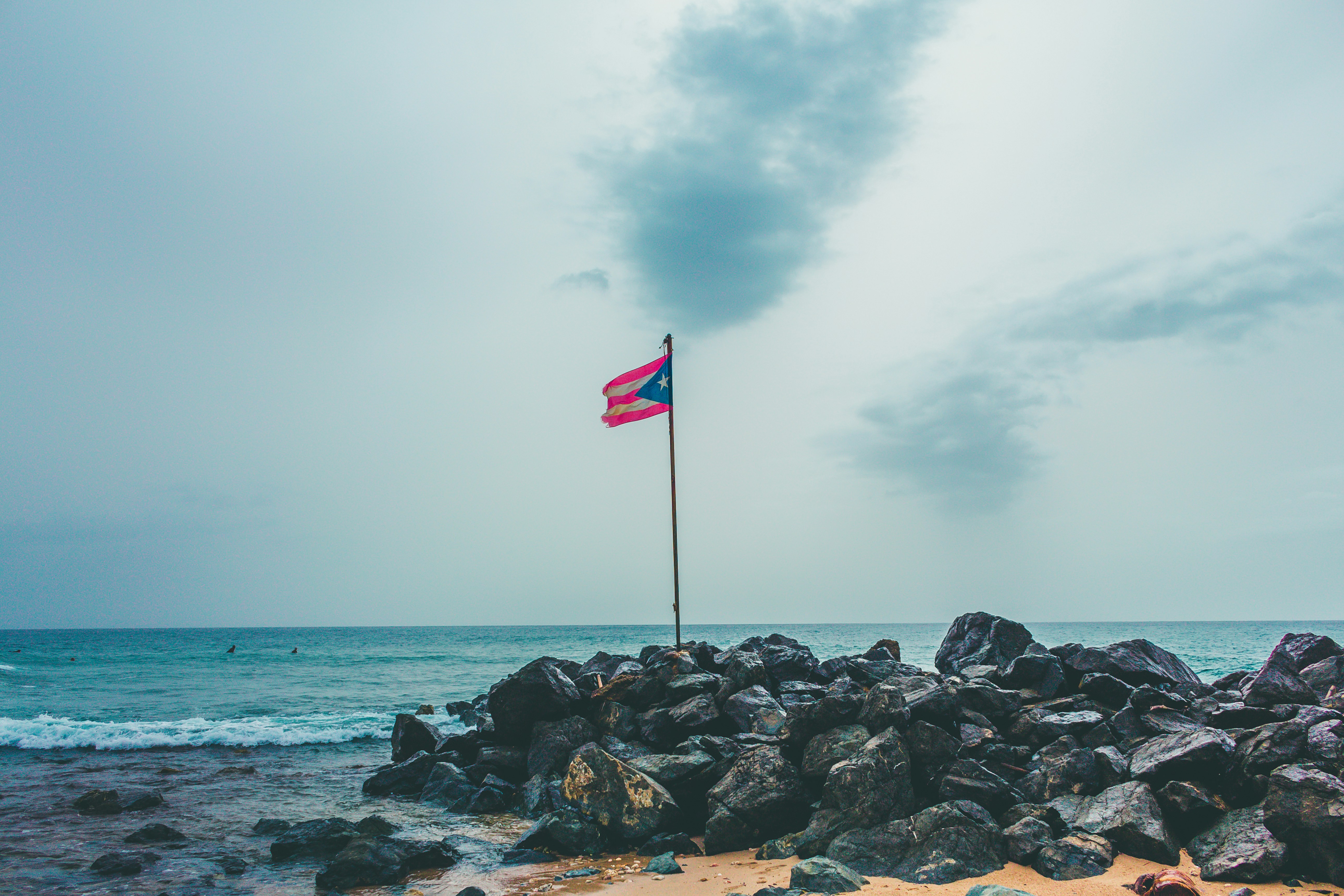 Una bandera en la roca cerca del mar bajo el cielo nublado durante el ...