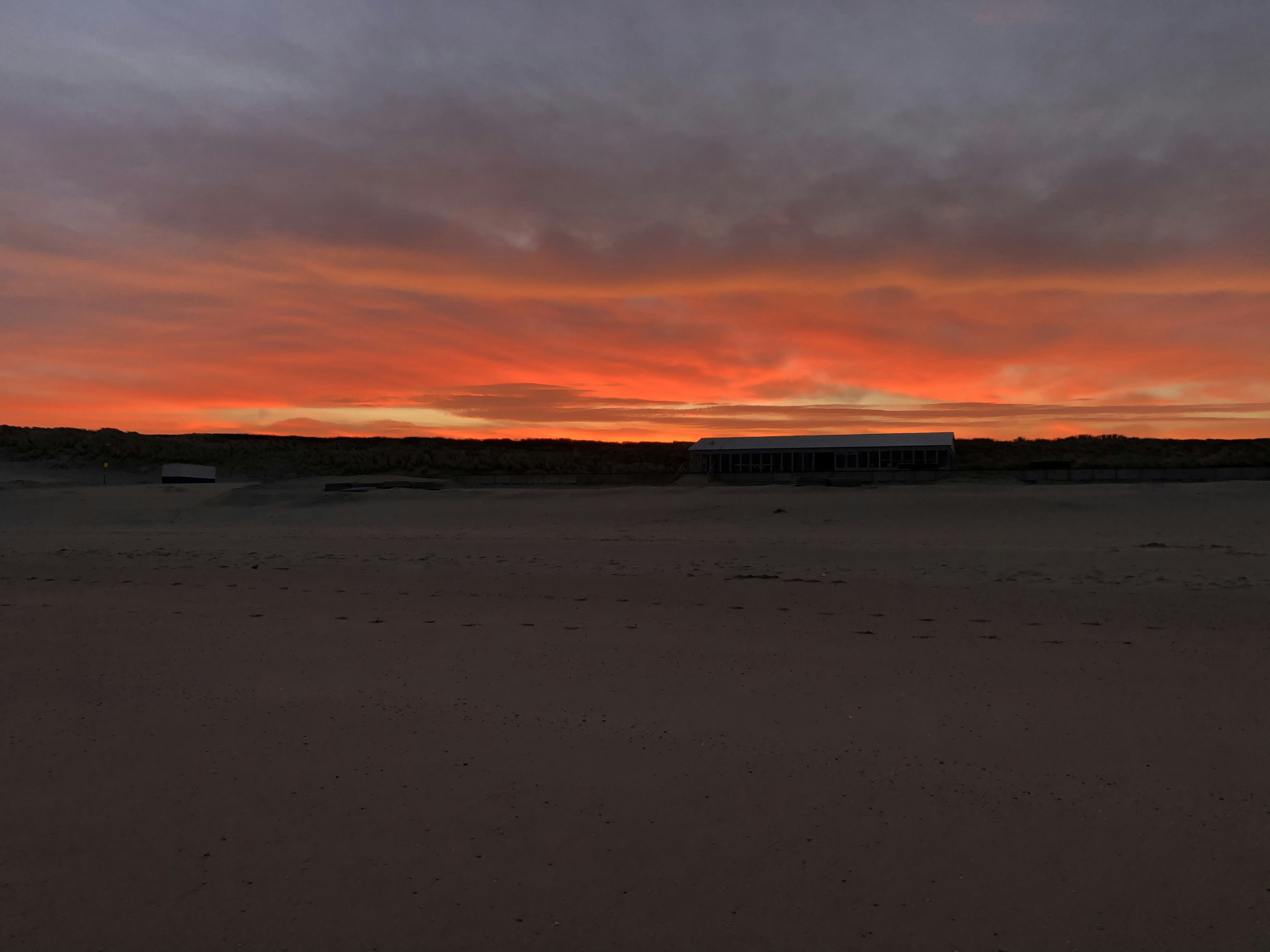Vibrant orange and red sunset over a calm, expansive landscape with a silhouetted horizon.